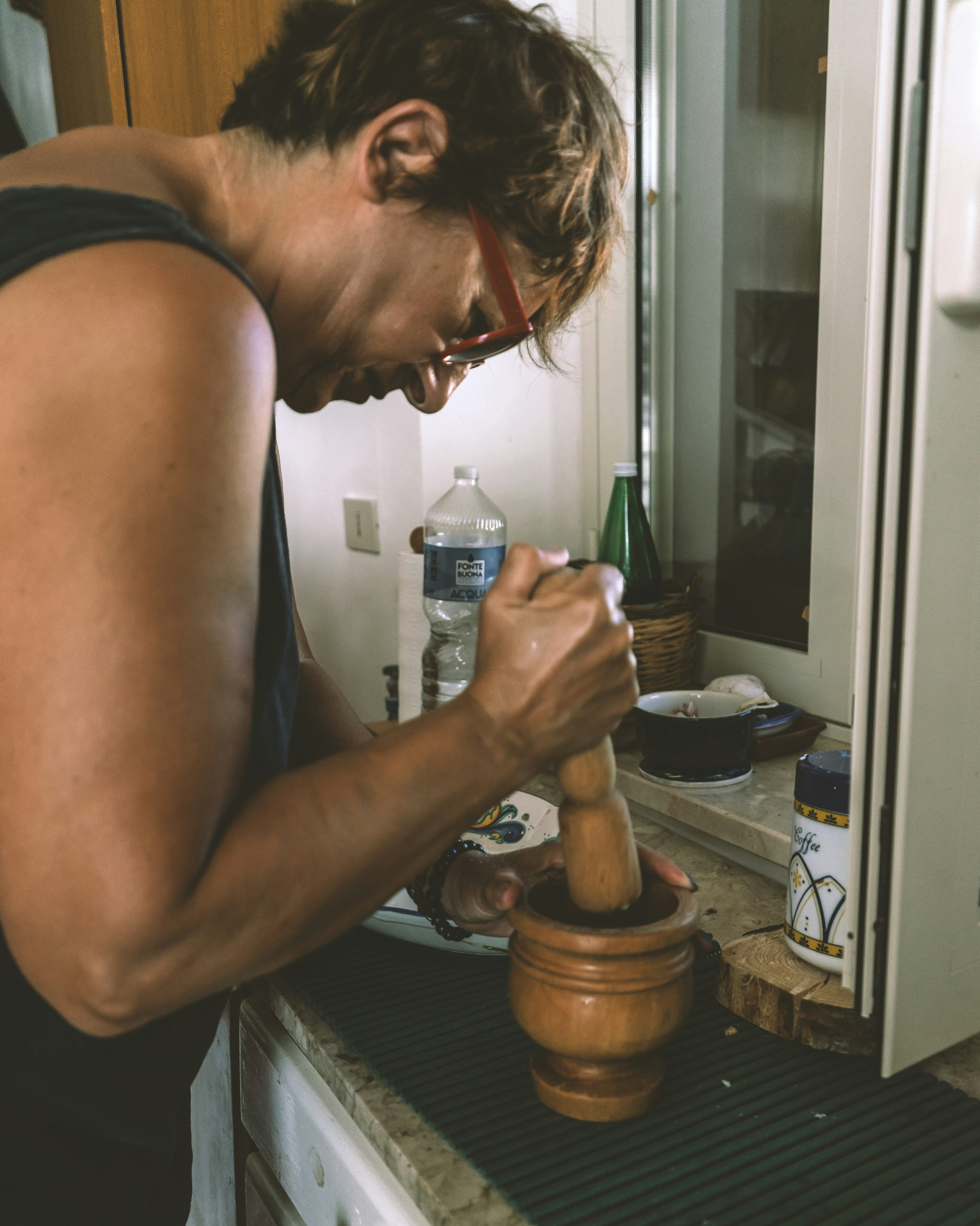 Person grinding spices in a wooden mortar and pestle in a cozy kitchen setting.