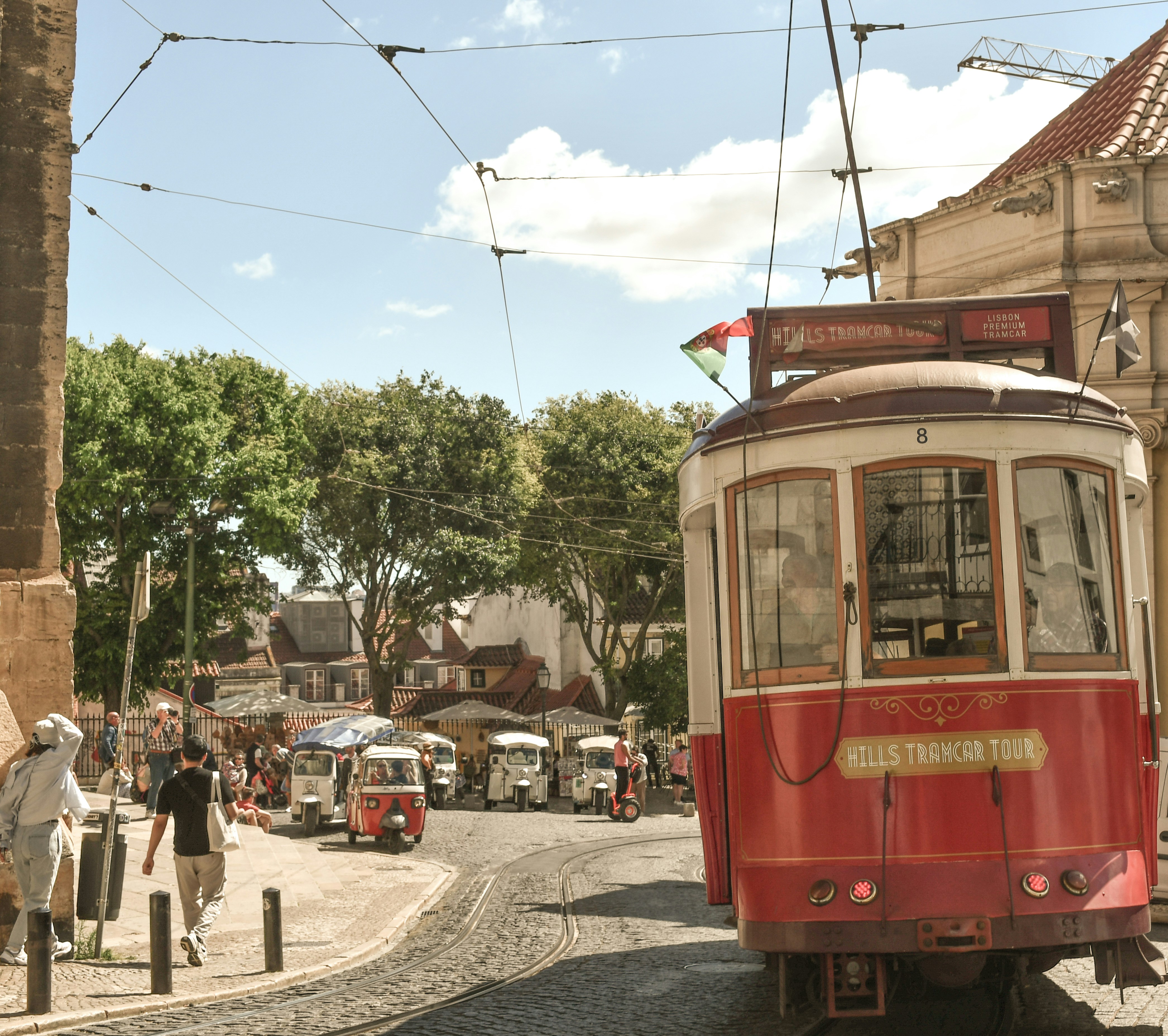 Red Tram Rounds a Historic Cobblestone Street Under a Tangle of Wires