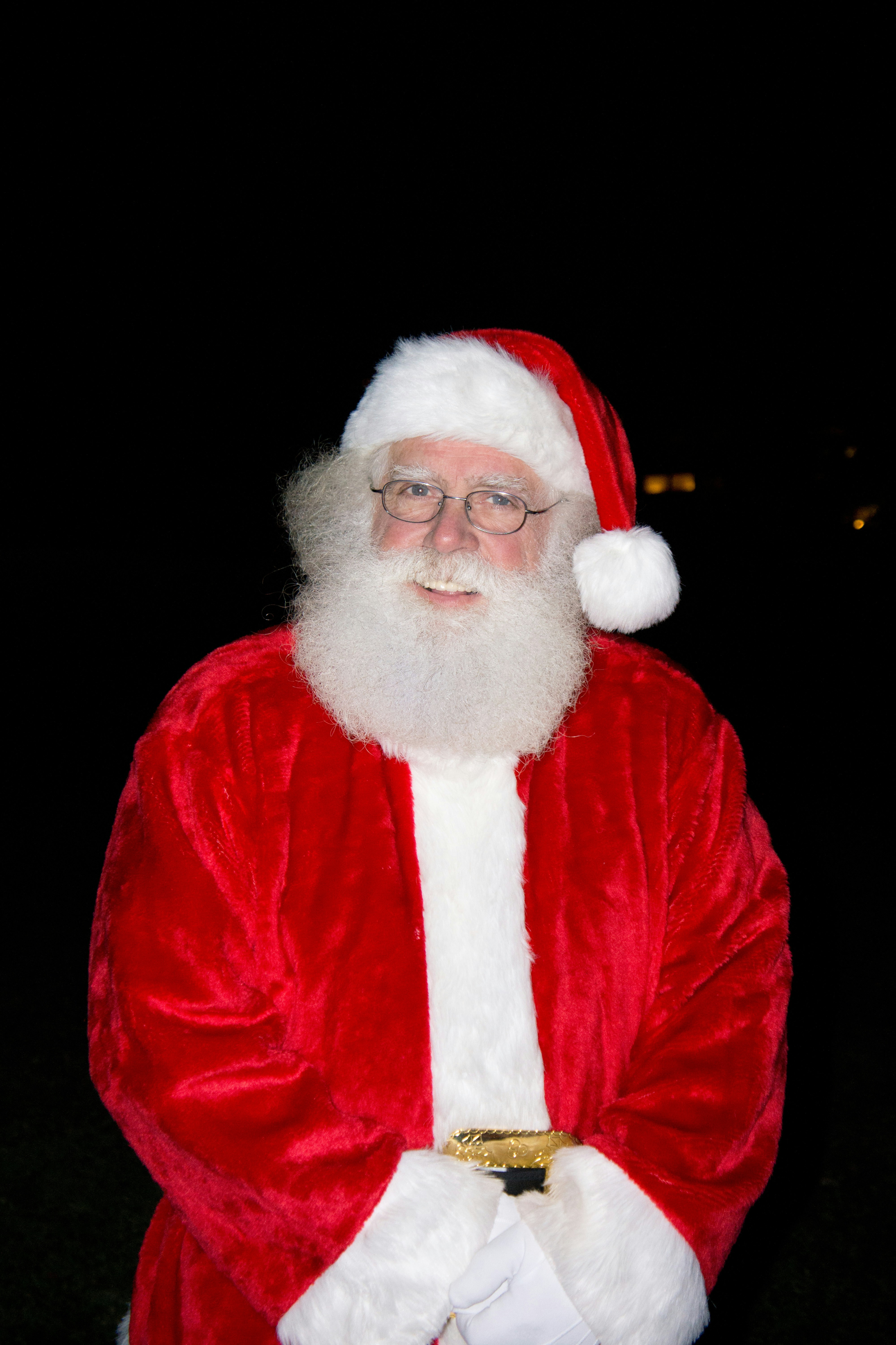 A cheerful figure in a red suit and white beard stands against a dark background, embodying the spirit of the holiday season.