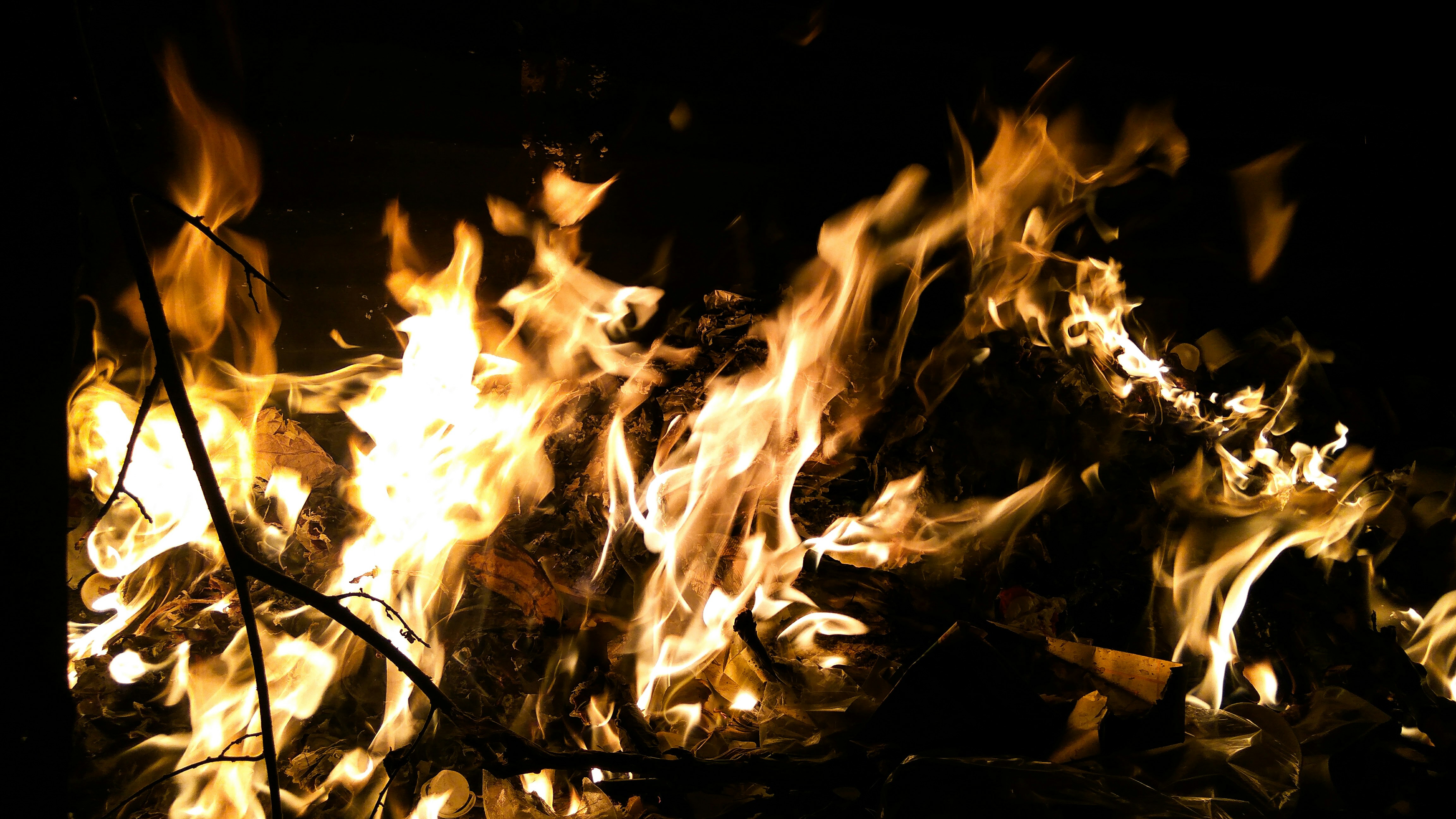 Vivid flames illuminating the darkness, with glowing embers and charred branches.
