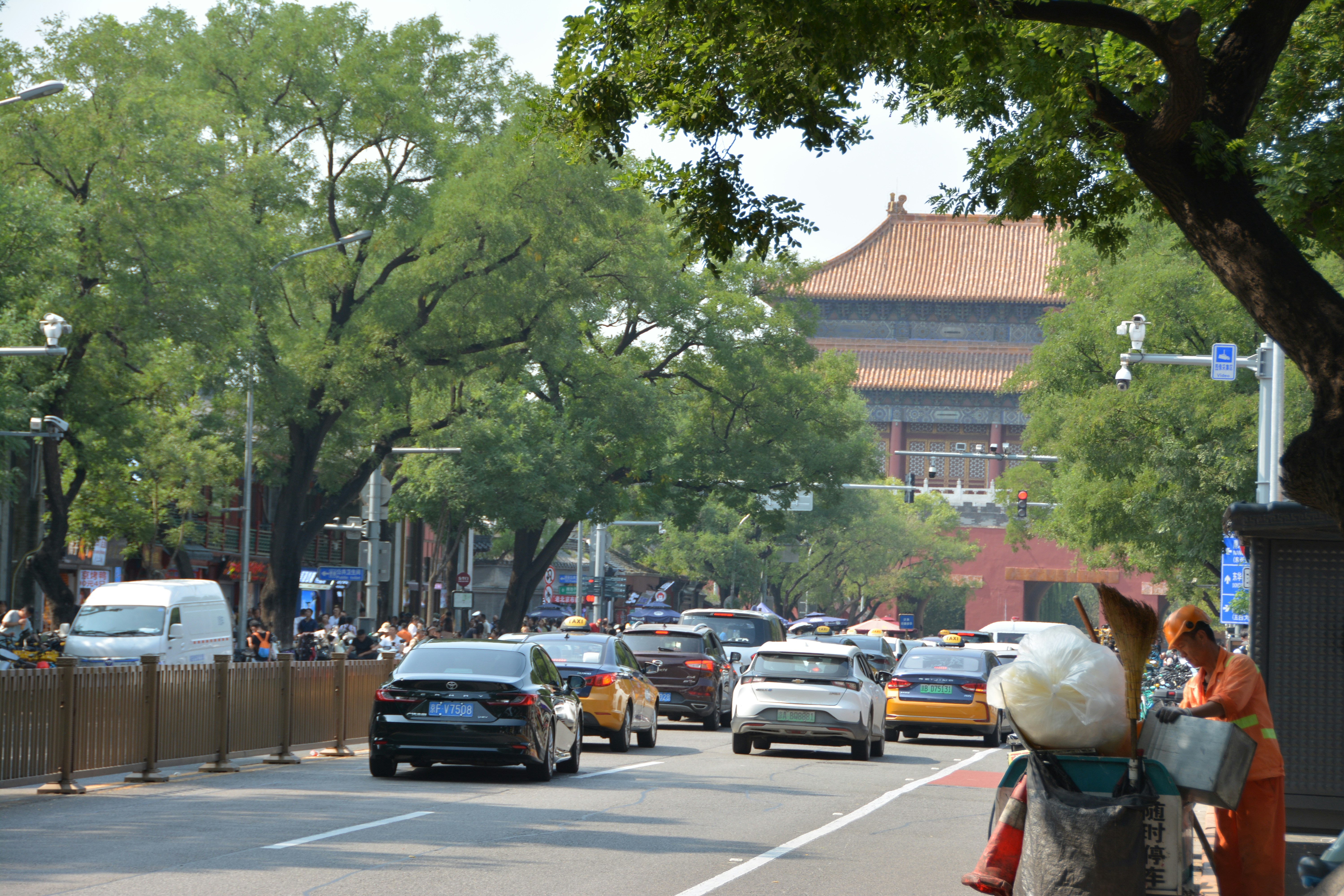 Busy street near the Forbidden City in Beijing with cars and a person collecting recyclables in the foreground.