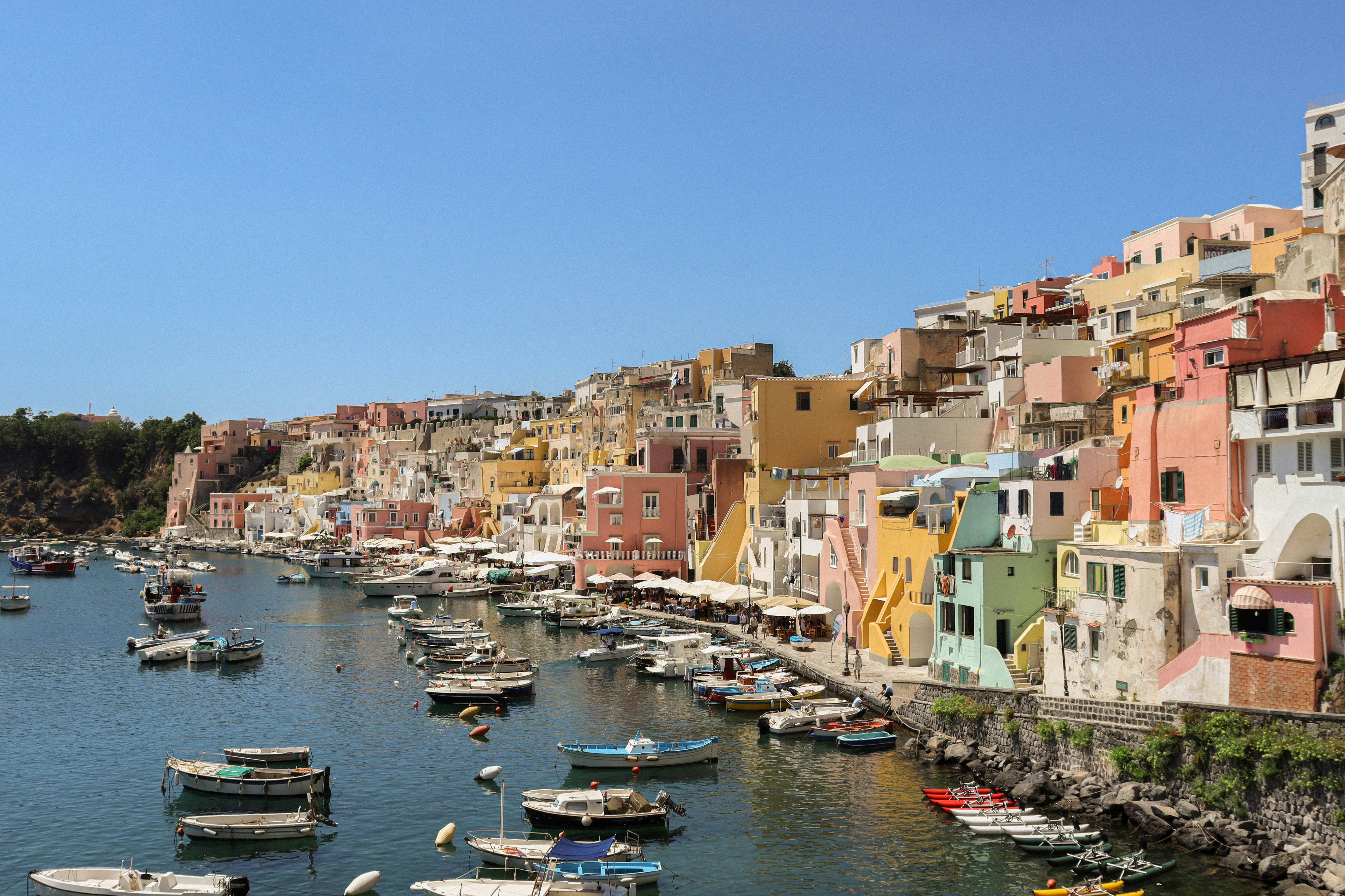 Colorful buildings line the waterfront of a harbor filled with small boats under a clear blue sky.