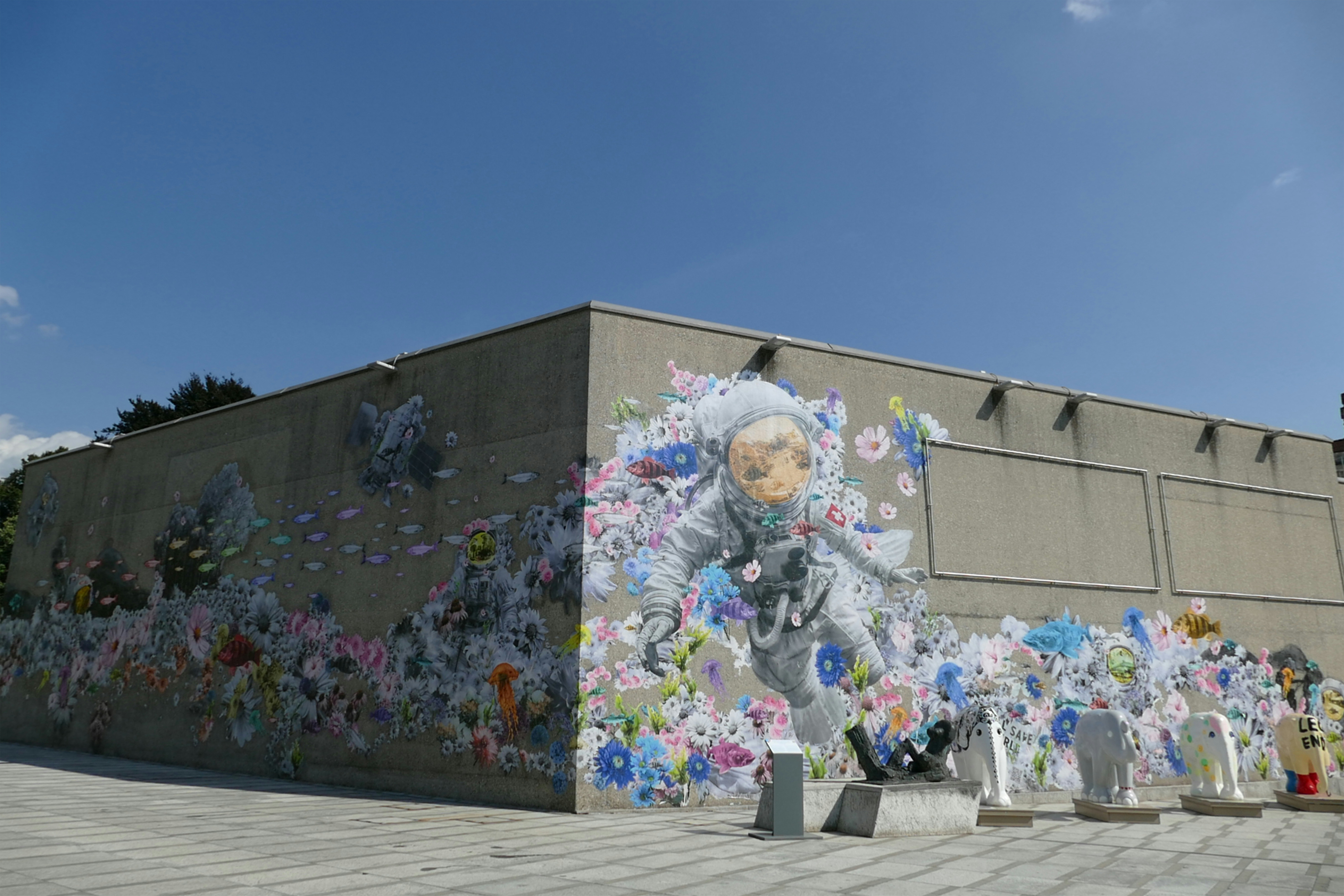 Colorful mural on a concrete wall featuring an astronaut surrounded by a vibrant bouquet of flowers. Public wall art blending space imagery with garden motifs.