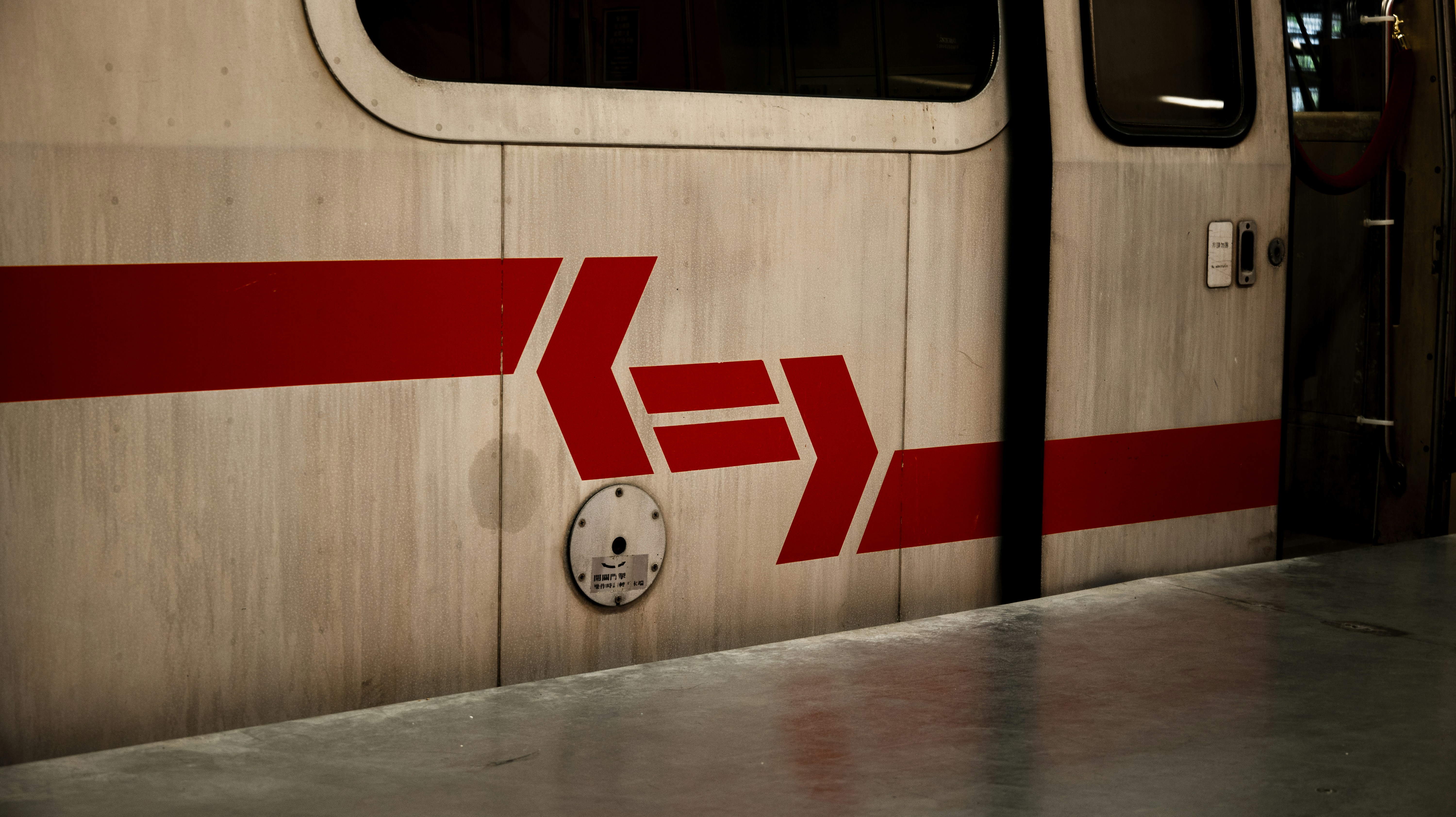 Weathered Transit Wall: Red Geometric Stripes Meet a Circular Hatch