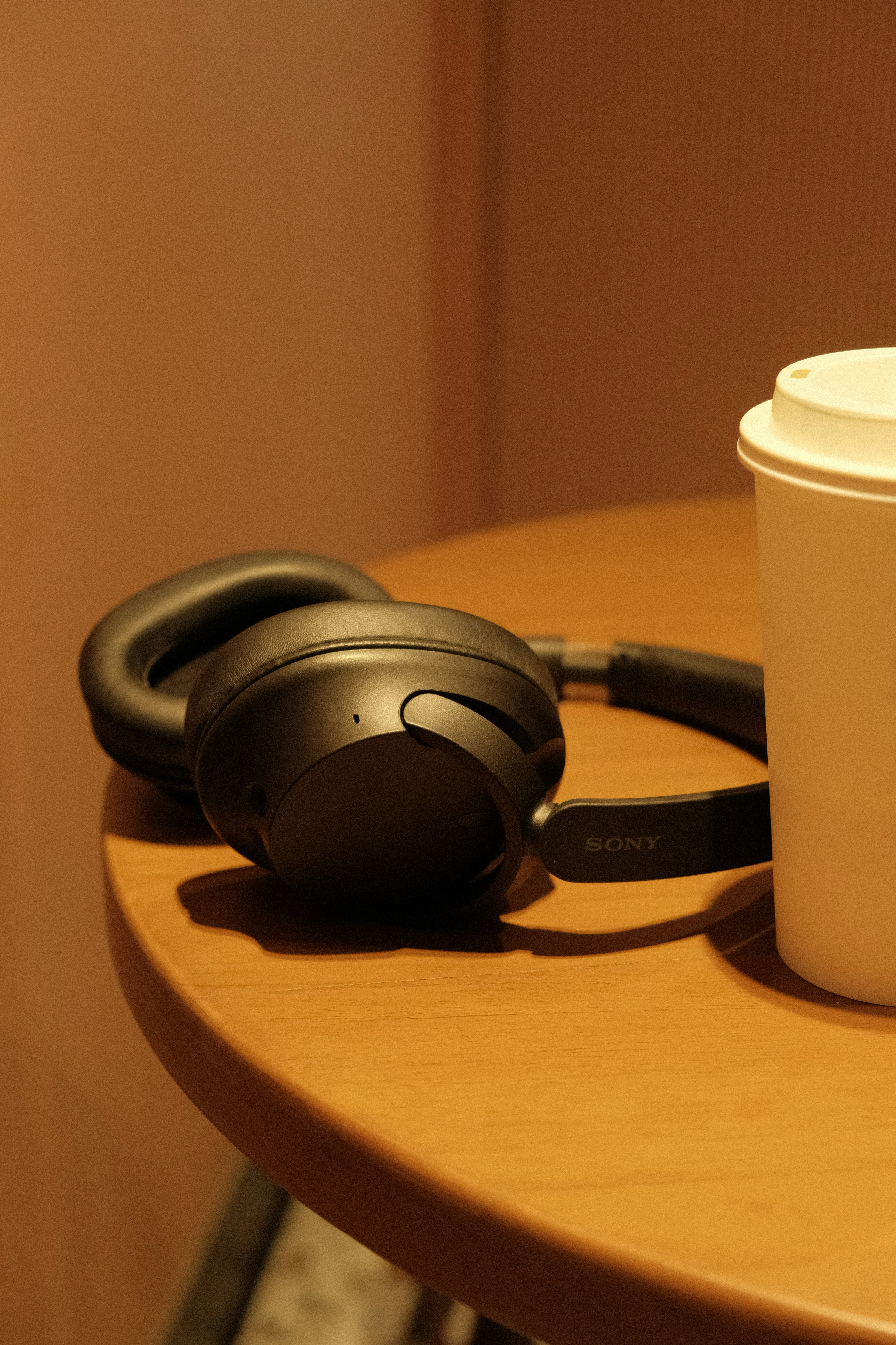 Quiet Studio Moment: Sony Headphones Rest Beside a Takeaway Cup on Warm Wood