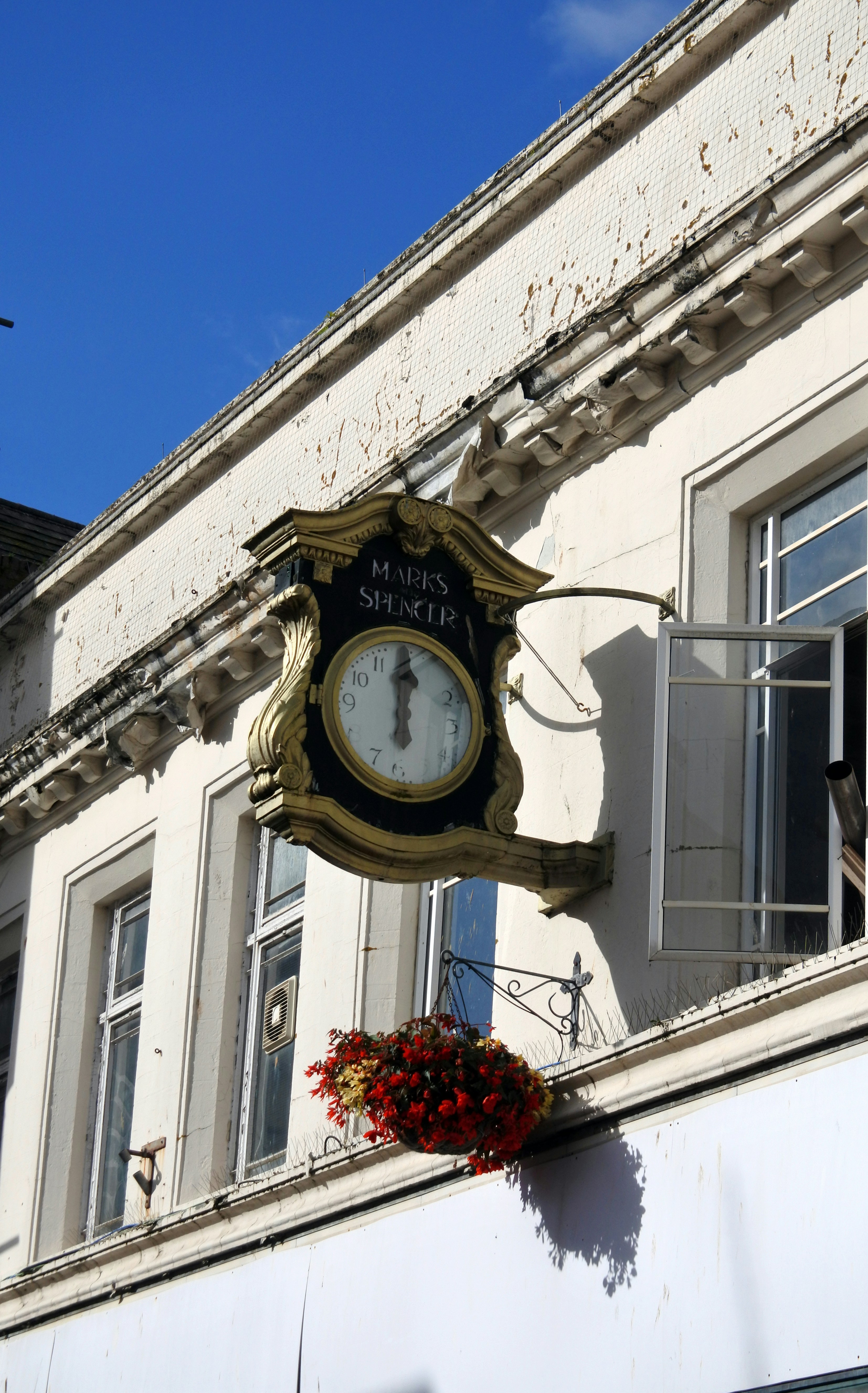 Ornate Clock Adorned with Hanging Crimson Blooms on a Historic Facade