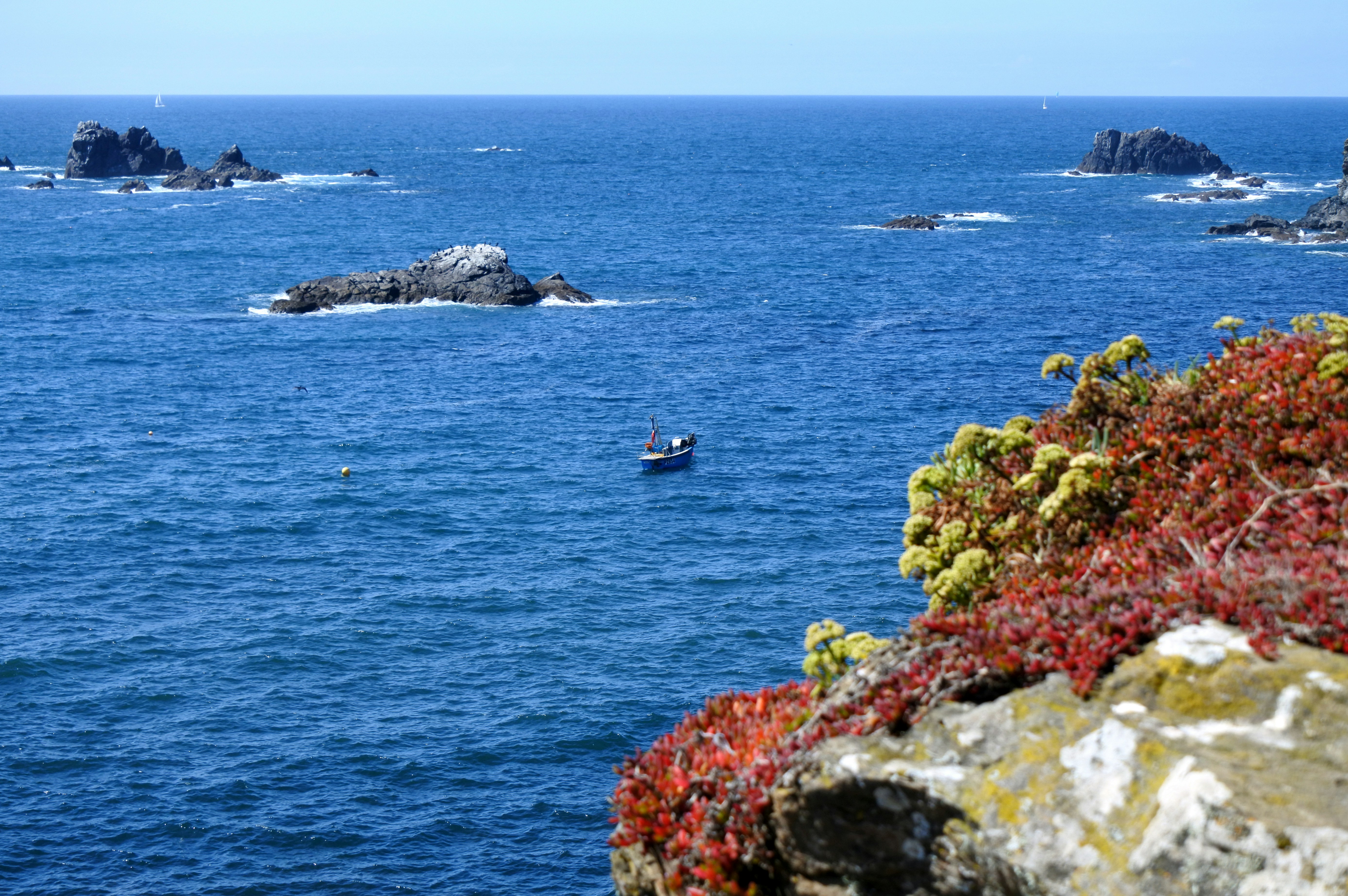 A Tiny Vessel Adrift in Indigo Waters Framed by Crimson Cliffside
