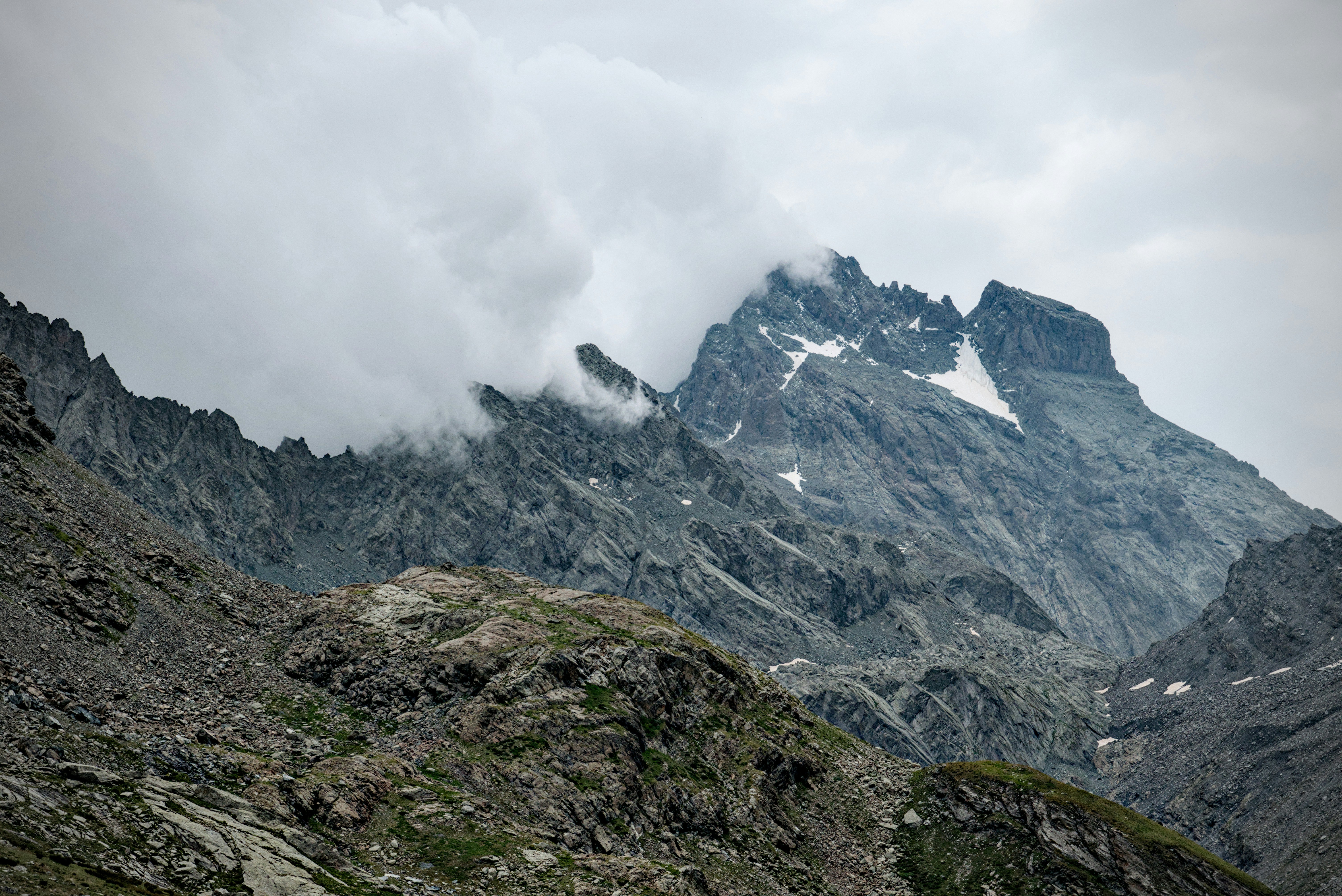 Jagged mountain peaks shrouded in swirling clouds under an overcast sky.