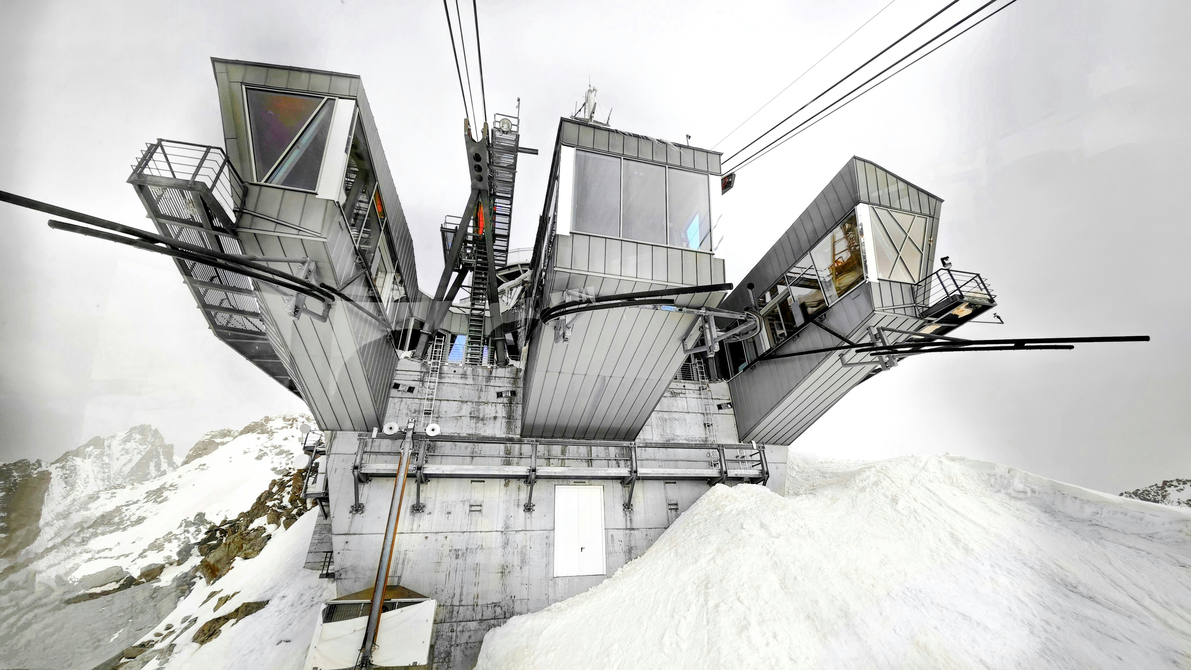 Modern architectural structure perched on a snowy mountain peak under a cloudy sky.