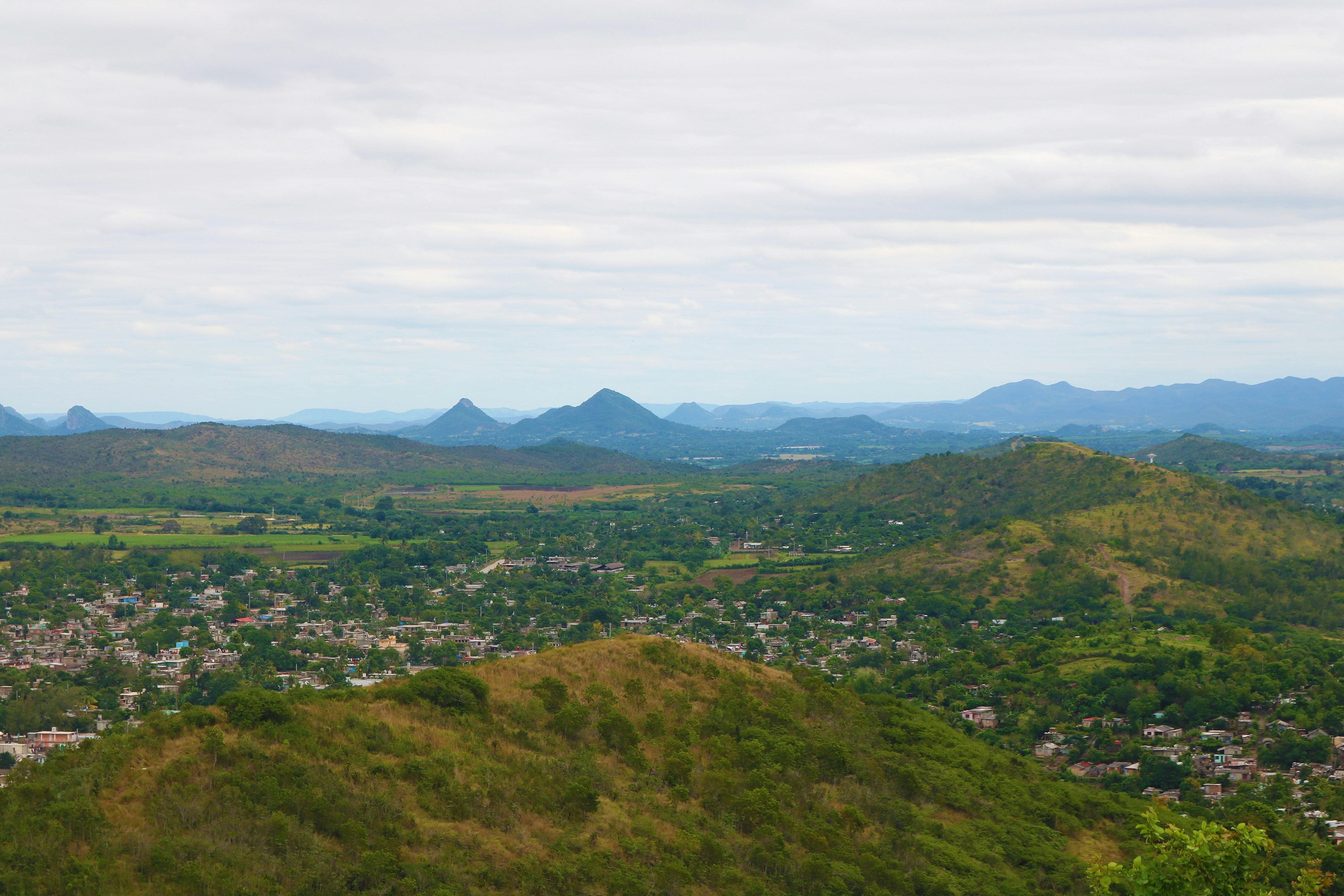 Expansive view of lush green hills with a distant mountain range under a cloudy sky.