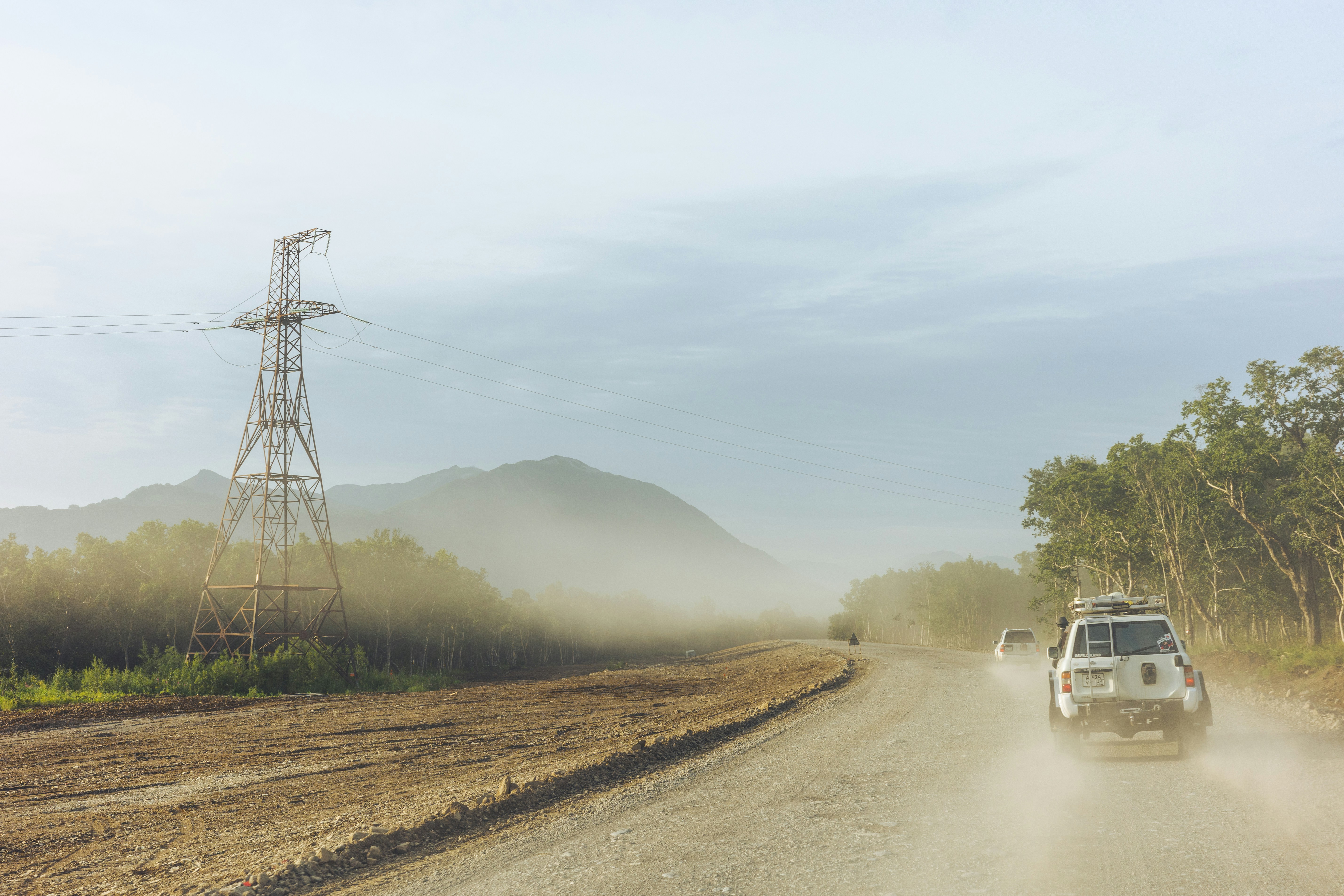 Dust Trail on the Open Road: A White SUV Drives Through a Sunlit Dust Cloud