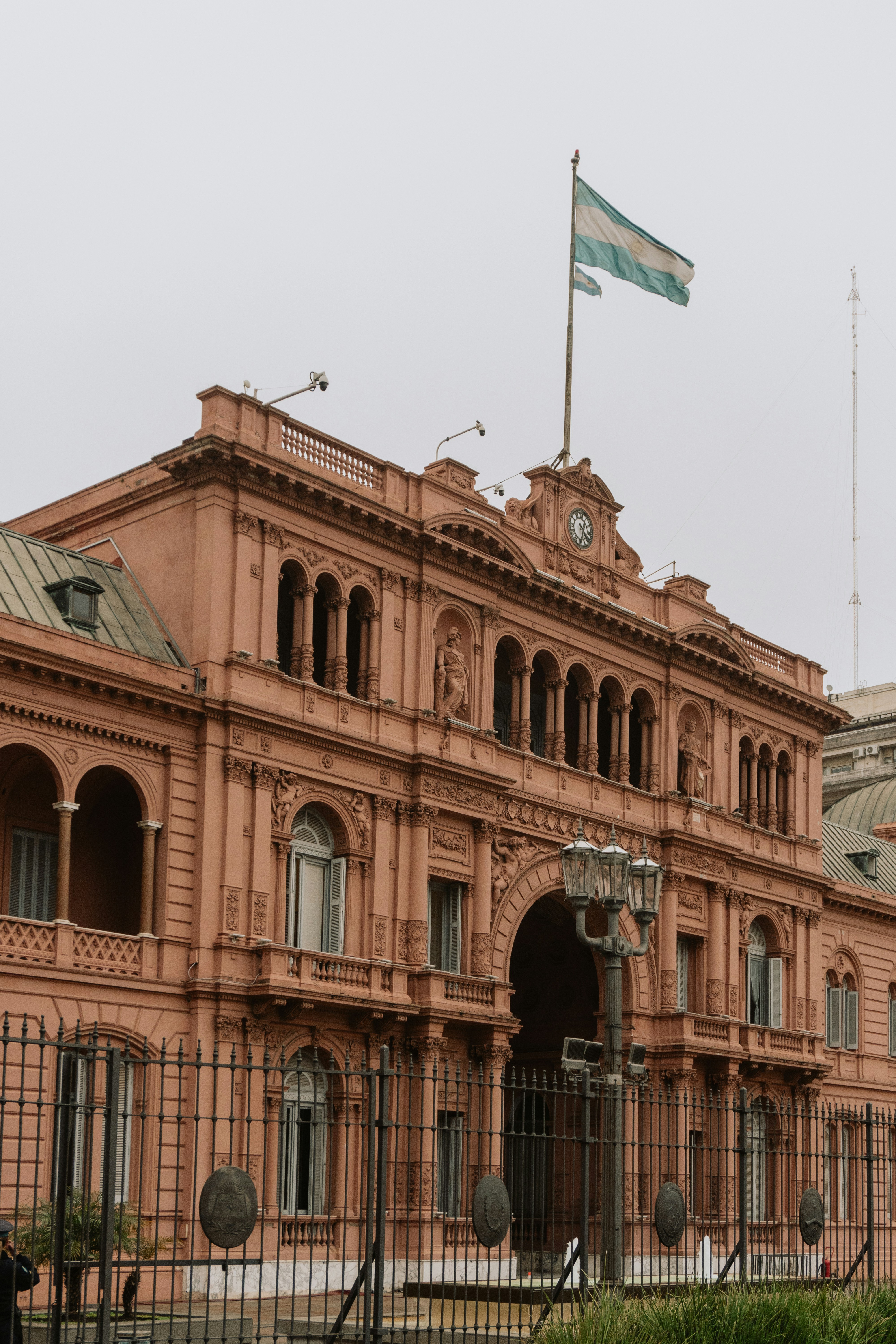 The Pink Facade: Central Archway, Clock, and Flag Above Ornate Ironwork
