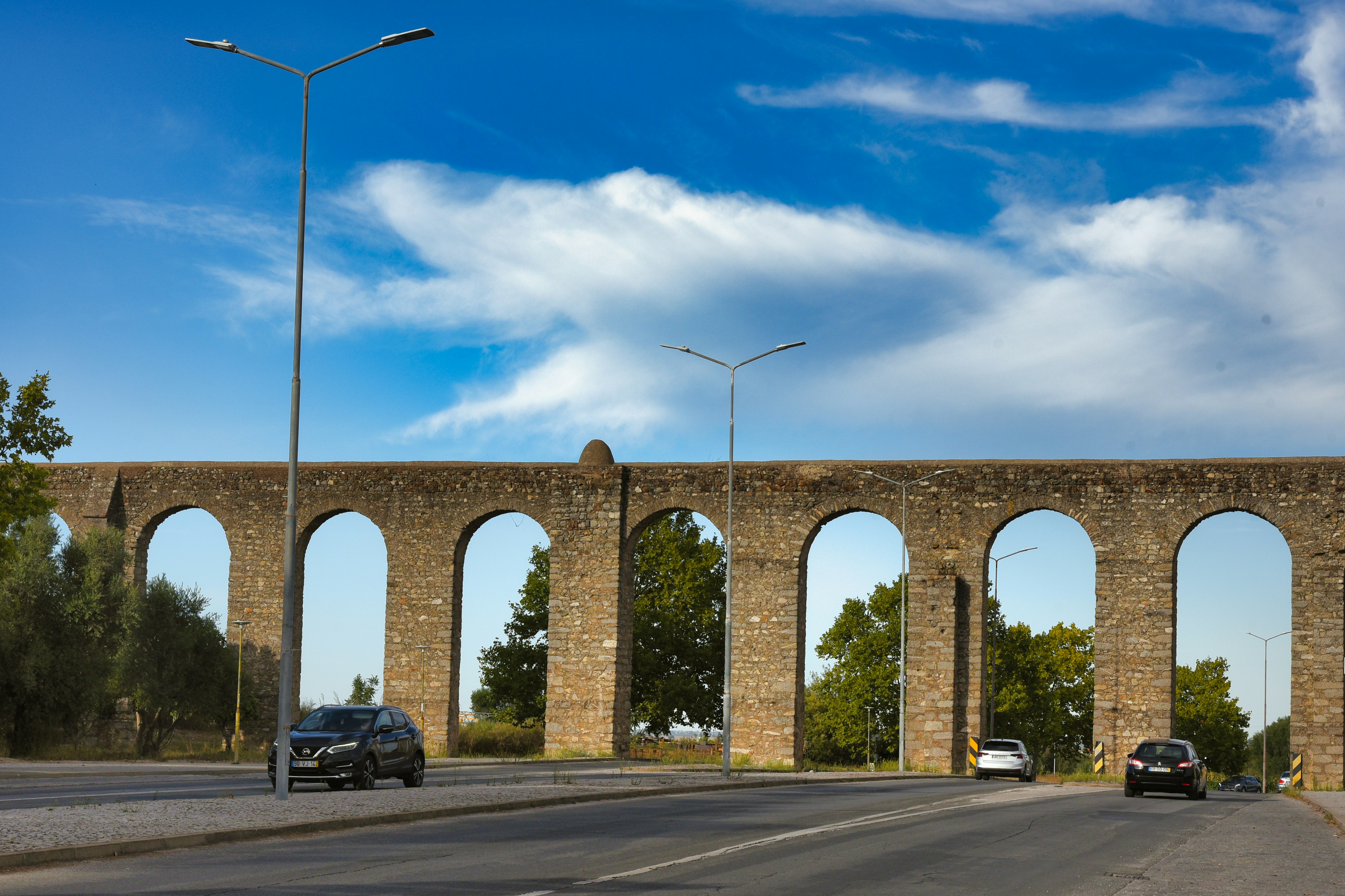 Sunlit Arches: Cars Thread the Stone Aqueduct Under a Clear Sky