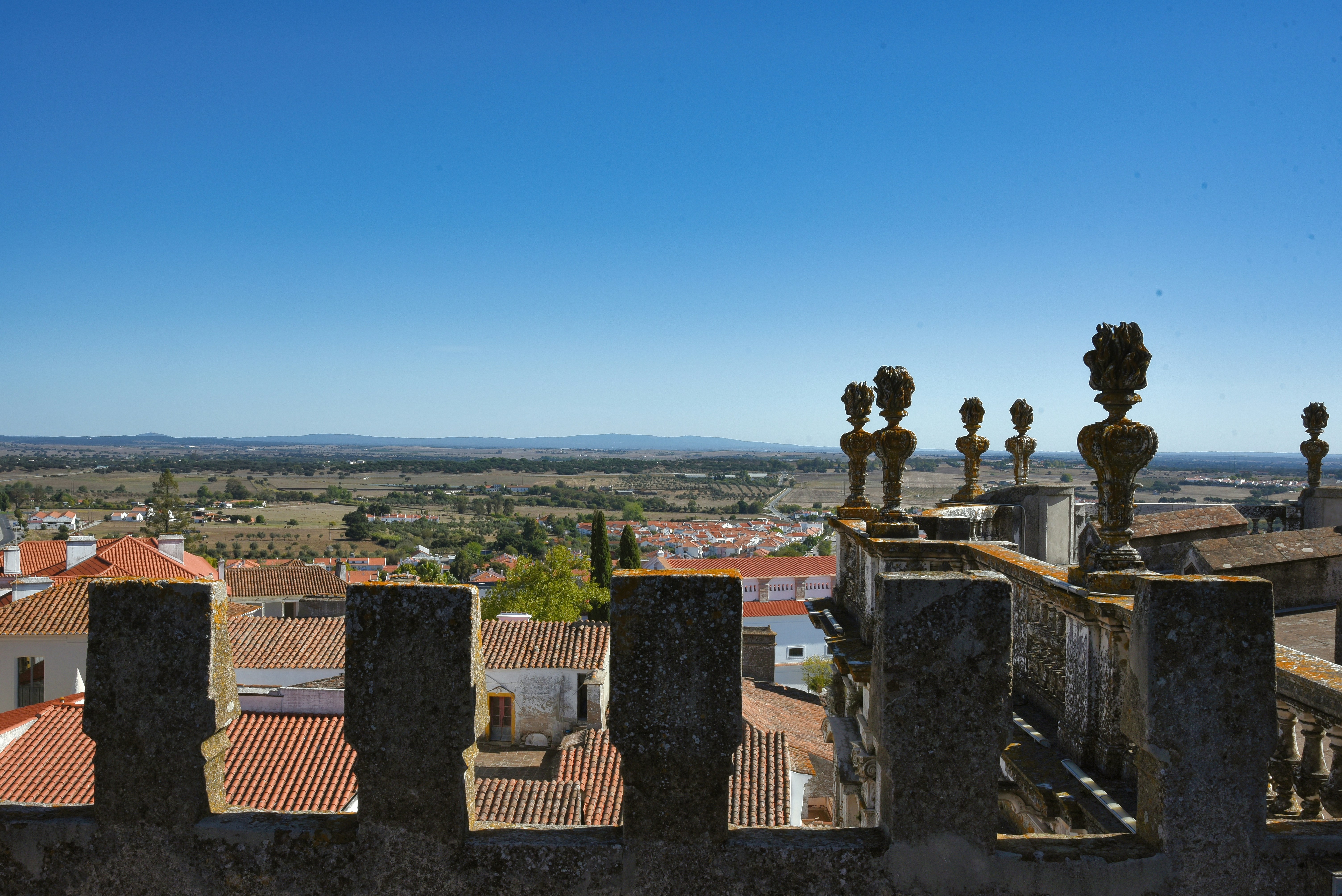 Ornate stone balustrade with decorative finials framing a panoramic view of rolling hills and a quaint town below.