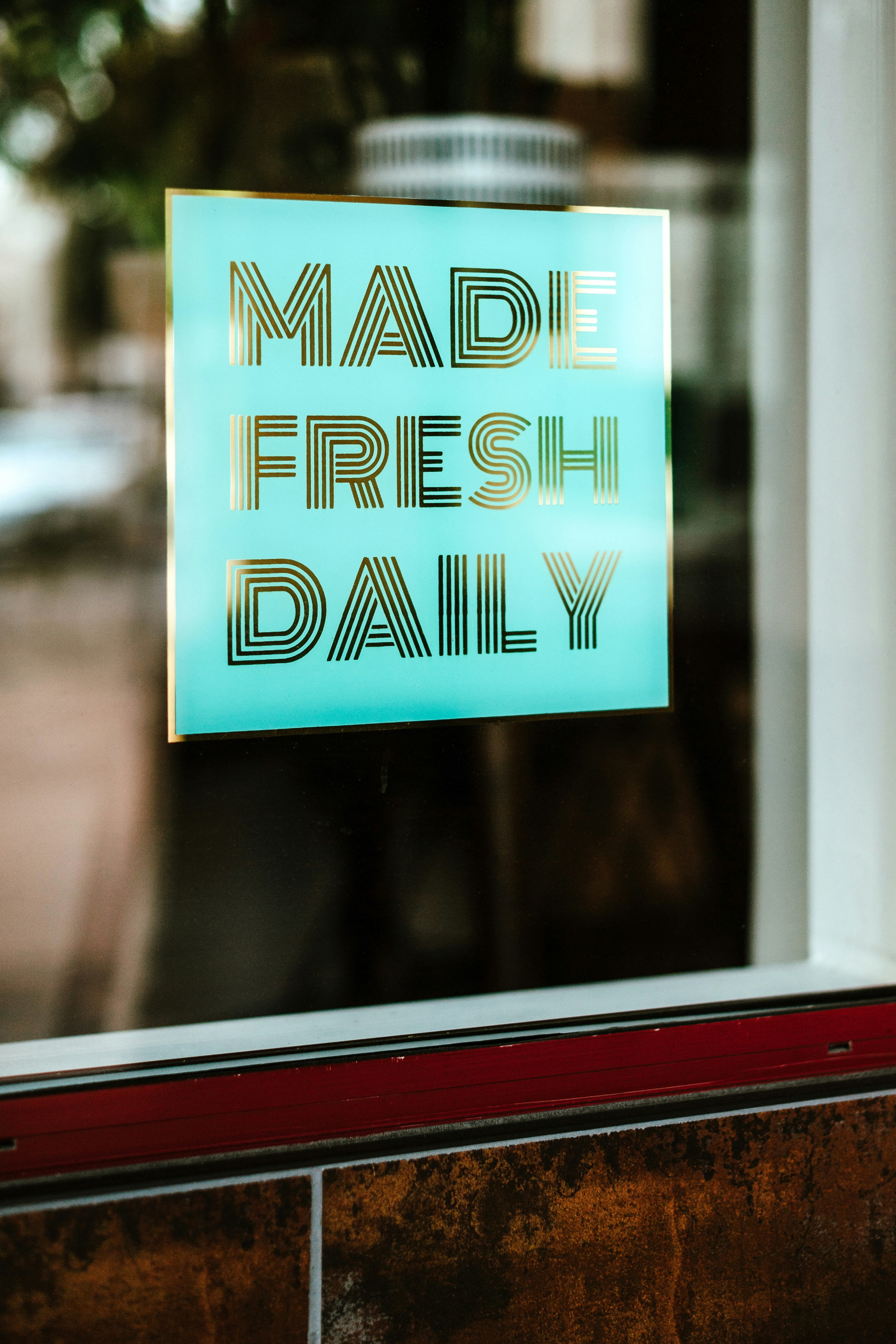 Sign with 'Made Fresh Daily' text on a window reflecting an urban scene.