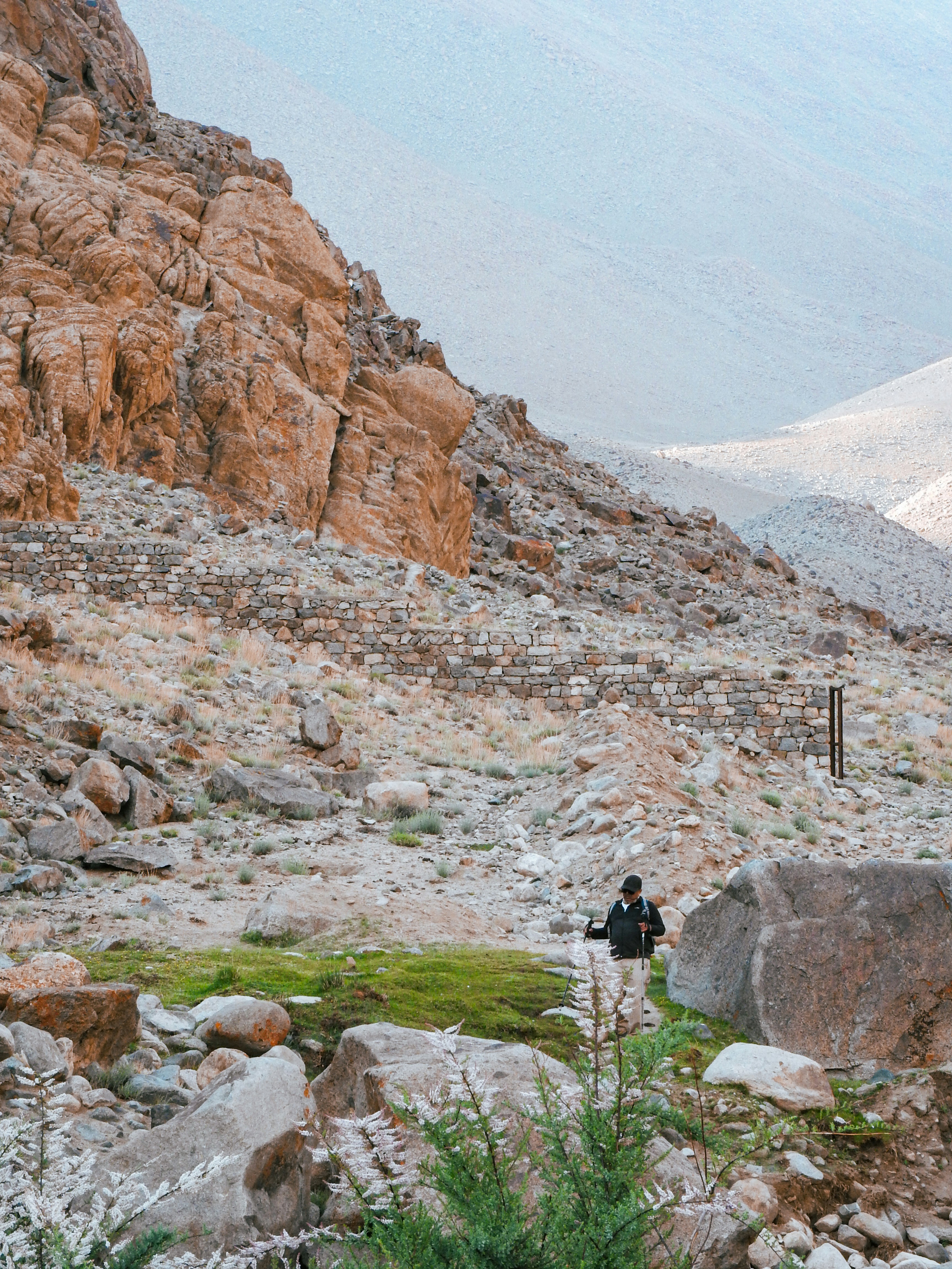 Explorer navigating rocky terrain near ancient stone structures amidst a vast, arid landscape.