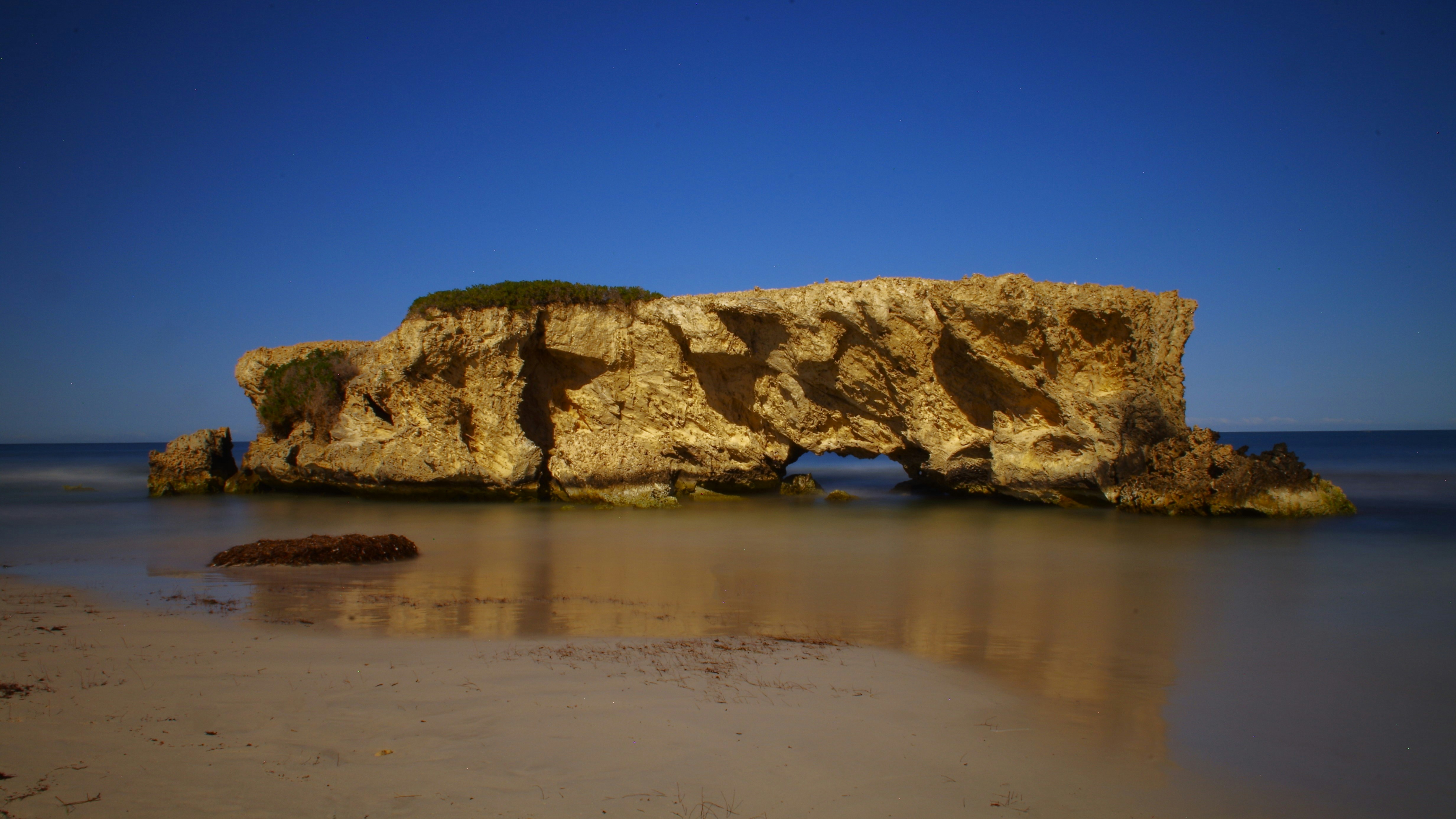 A rock sticking out of the water on a beach photo – Free Two rocks wa ...
