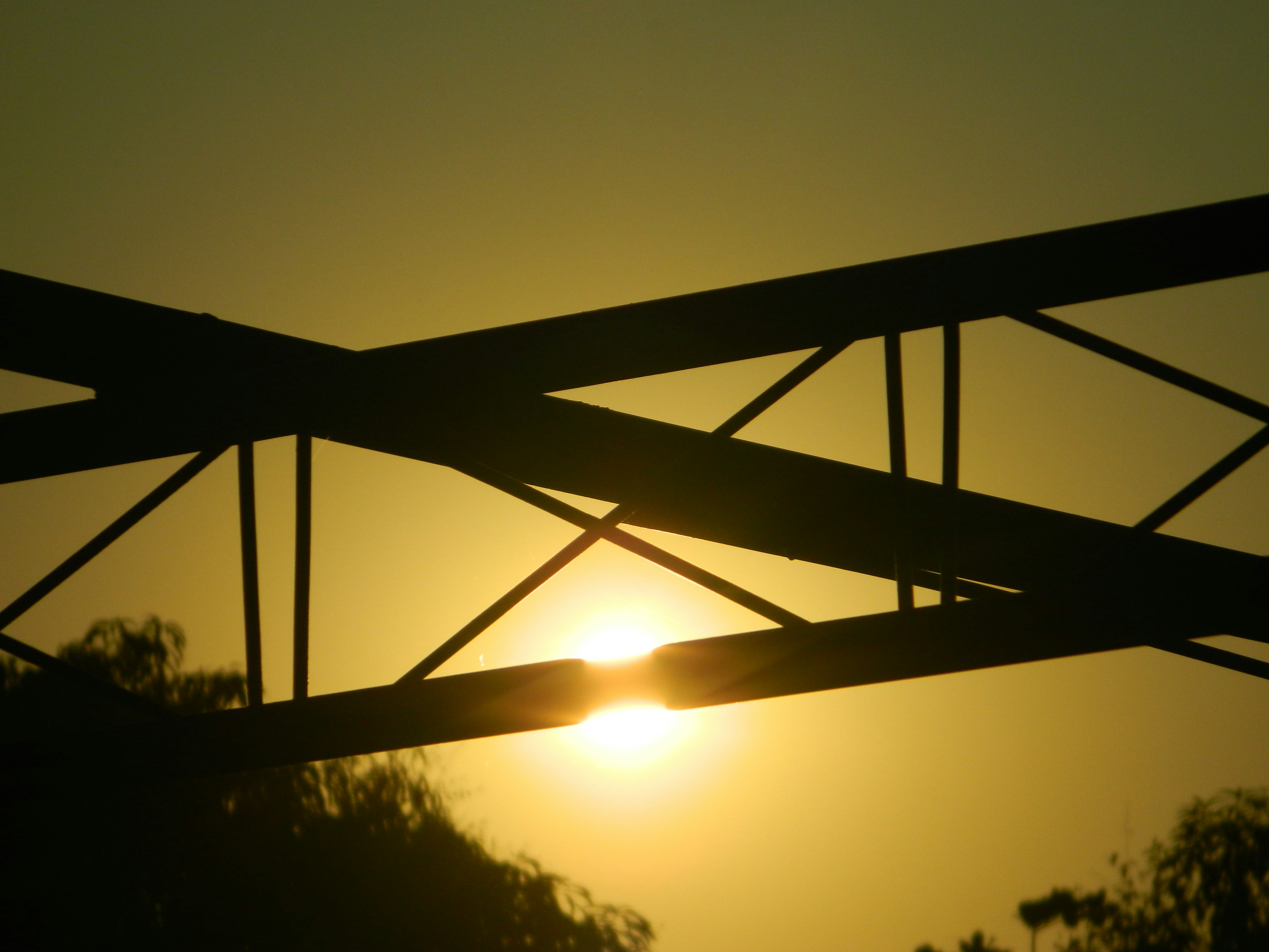 The sun is setting behind a metal bridge