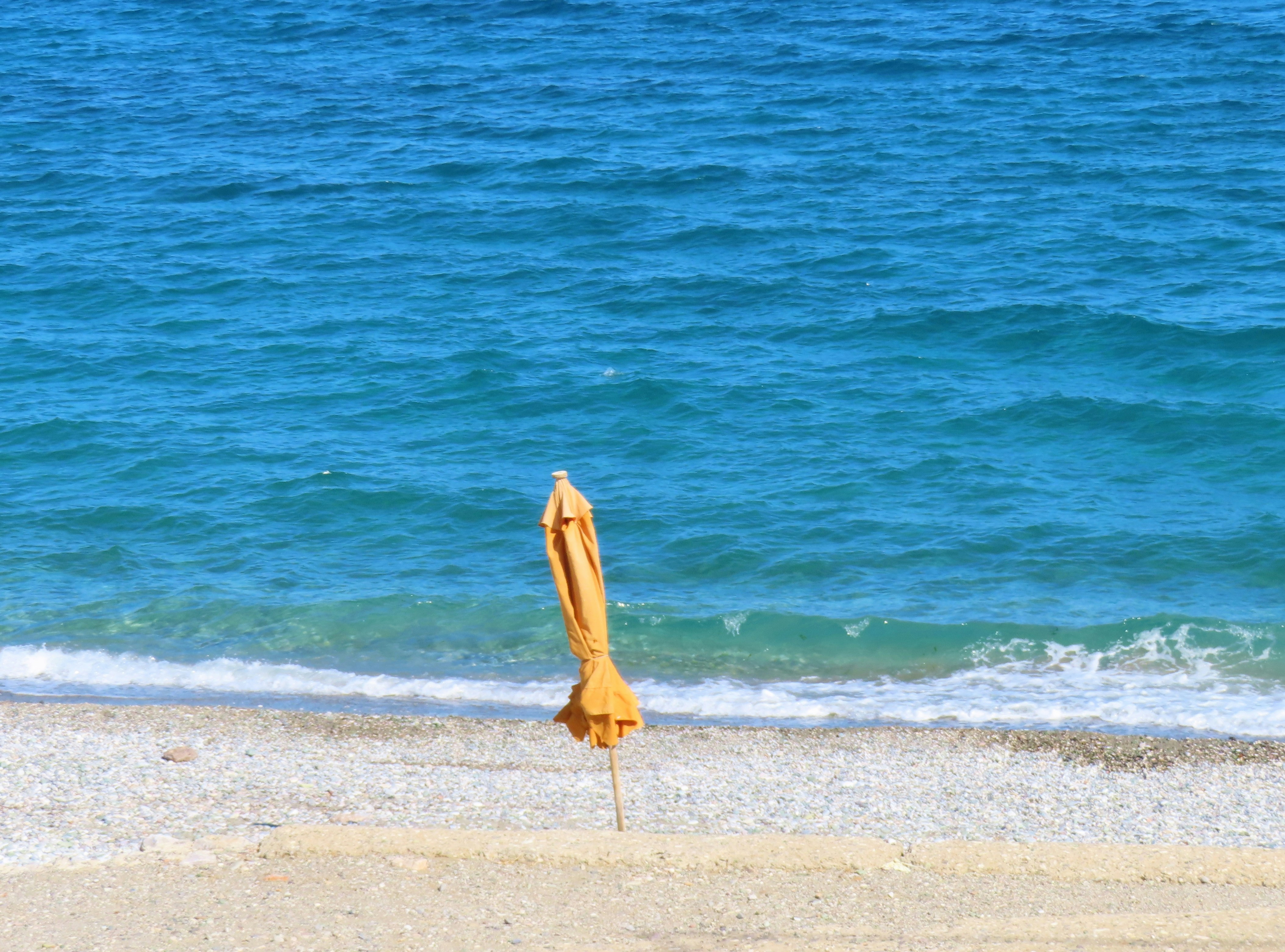 Solitary Orange Umbrella Framed by Pebbles and Turquoise Sea