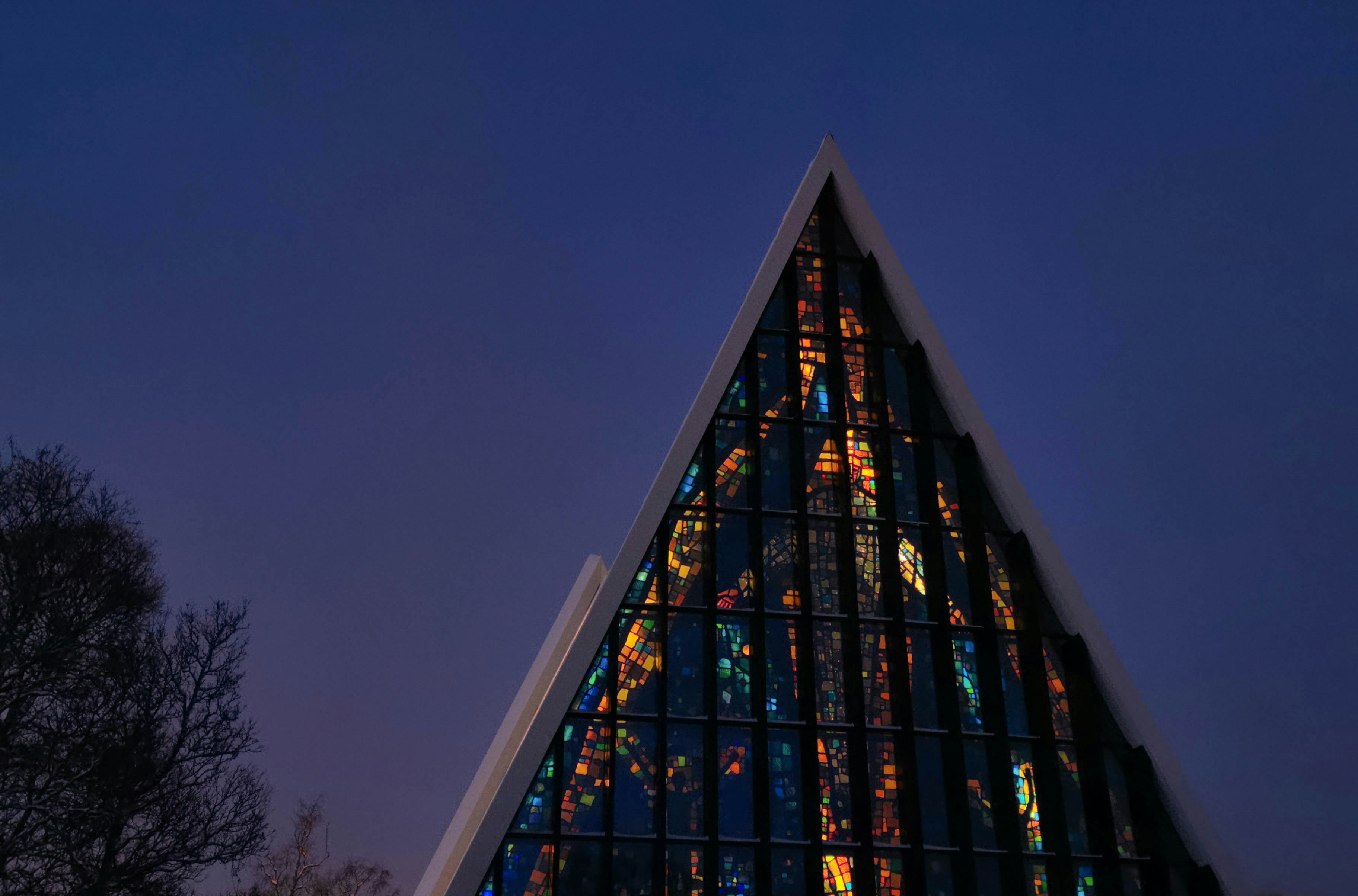 Triangular glass facade reflecting vibrant stained glass designs under twilight sky.