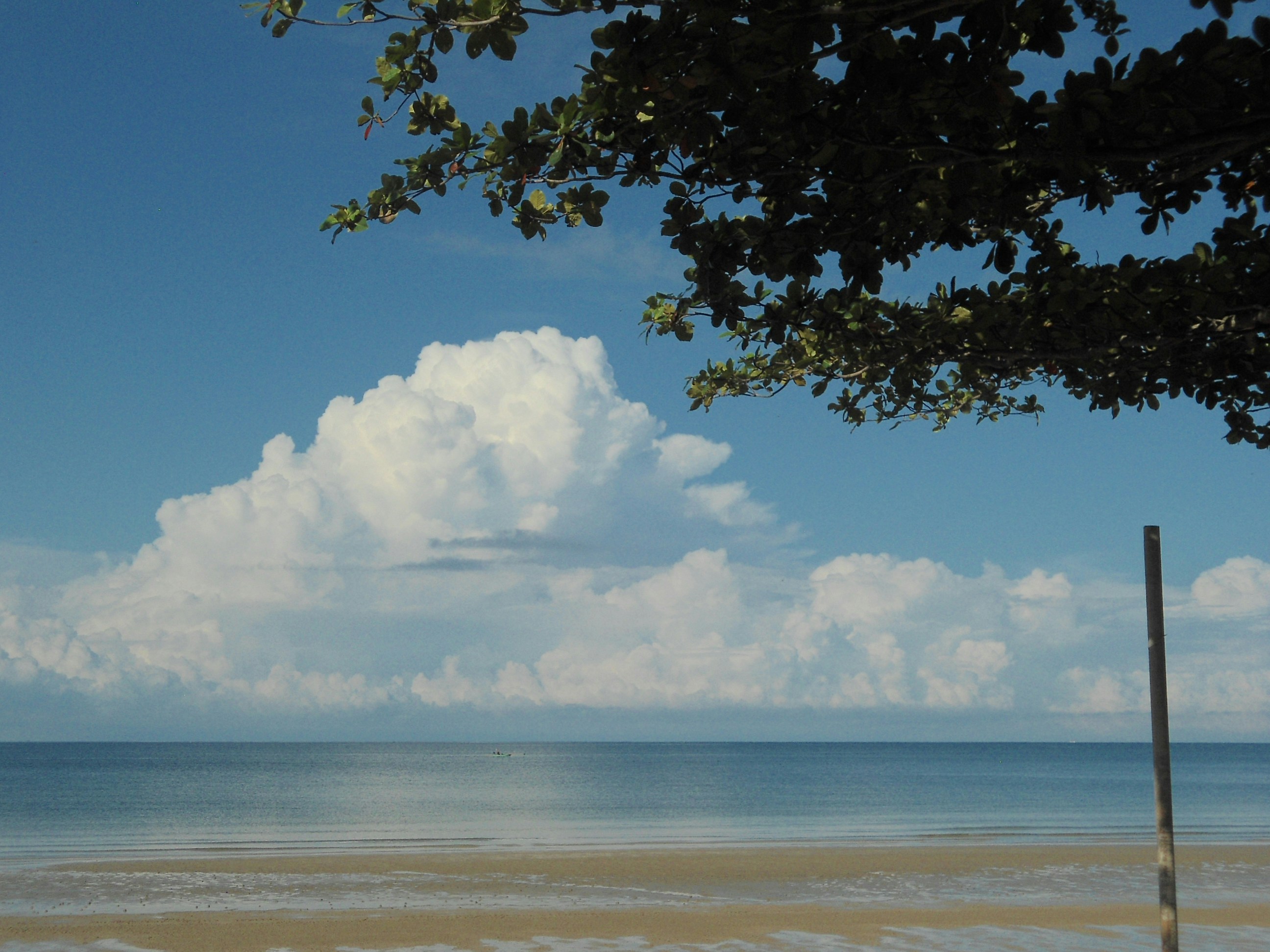 Clouds billow over a tranquil sea with tree branches framing the view at Chao Lao Beach.