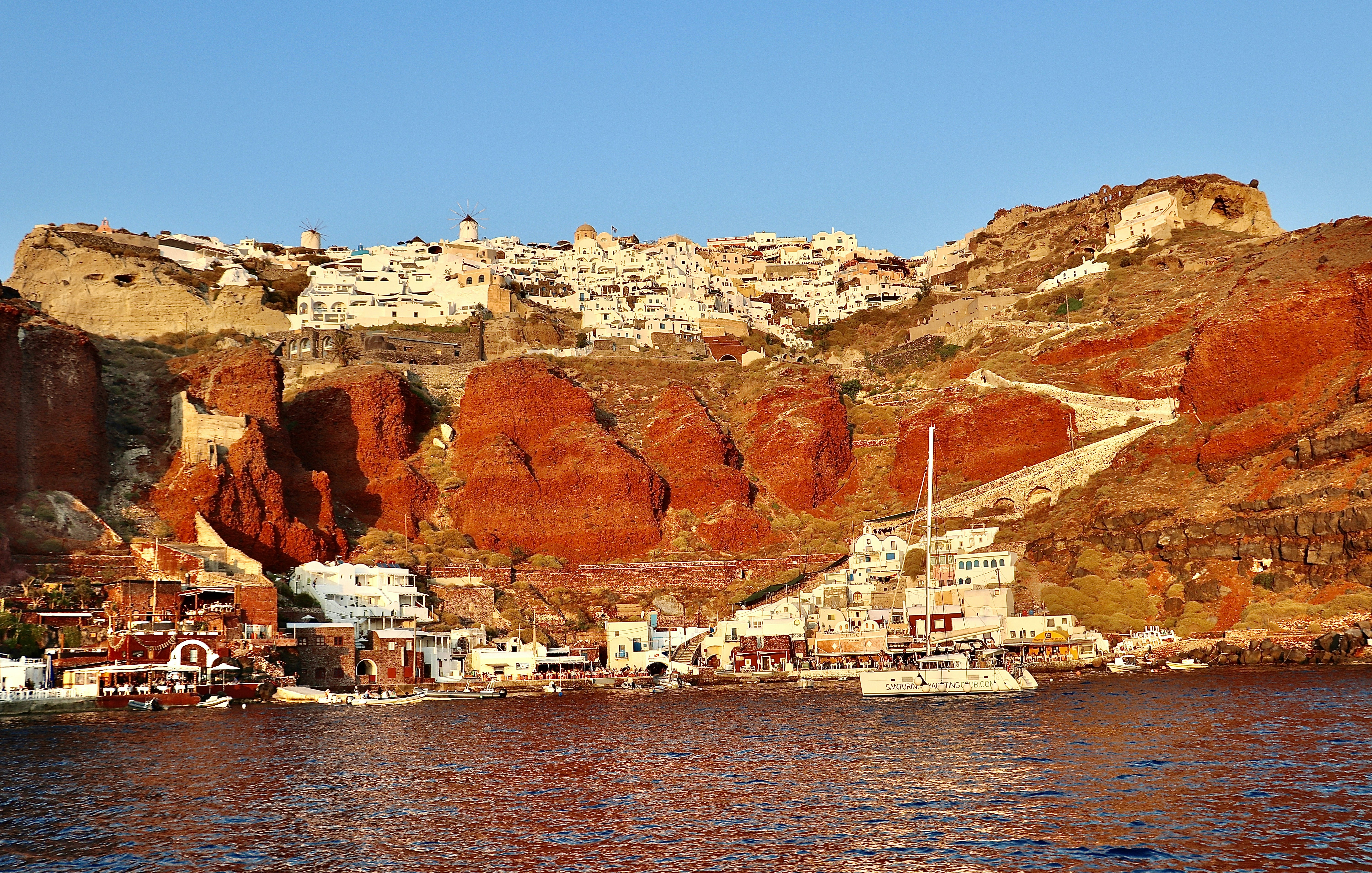 Whitewashed Town Aloft on Ember-Red Cliffs Over a Tranquil Aegean Harbor