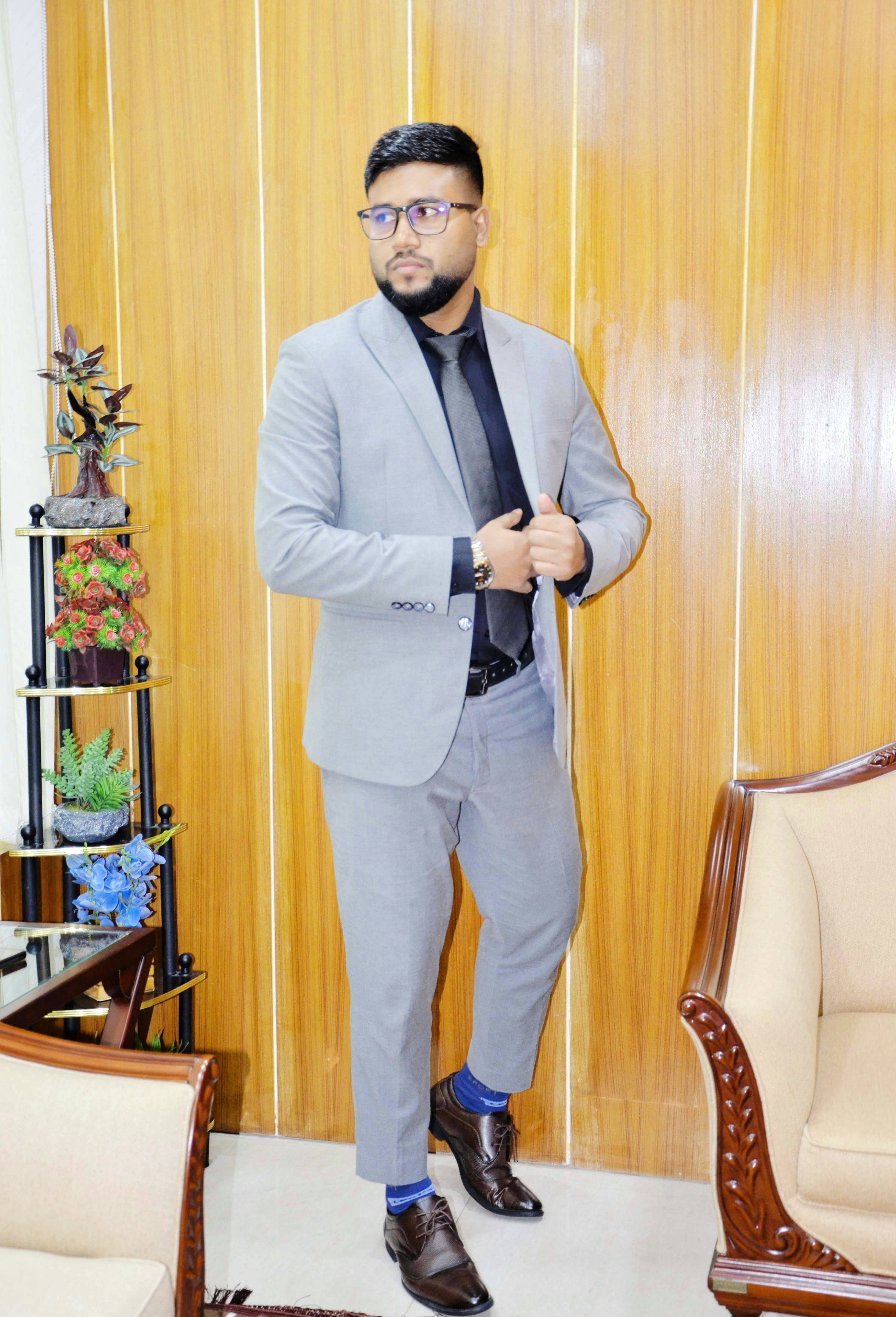 A well-dressed individual in a tailored gray suit stands confidently against a wooden backdrop, showcasing a blend of style and professionalism.