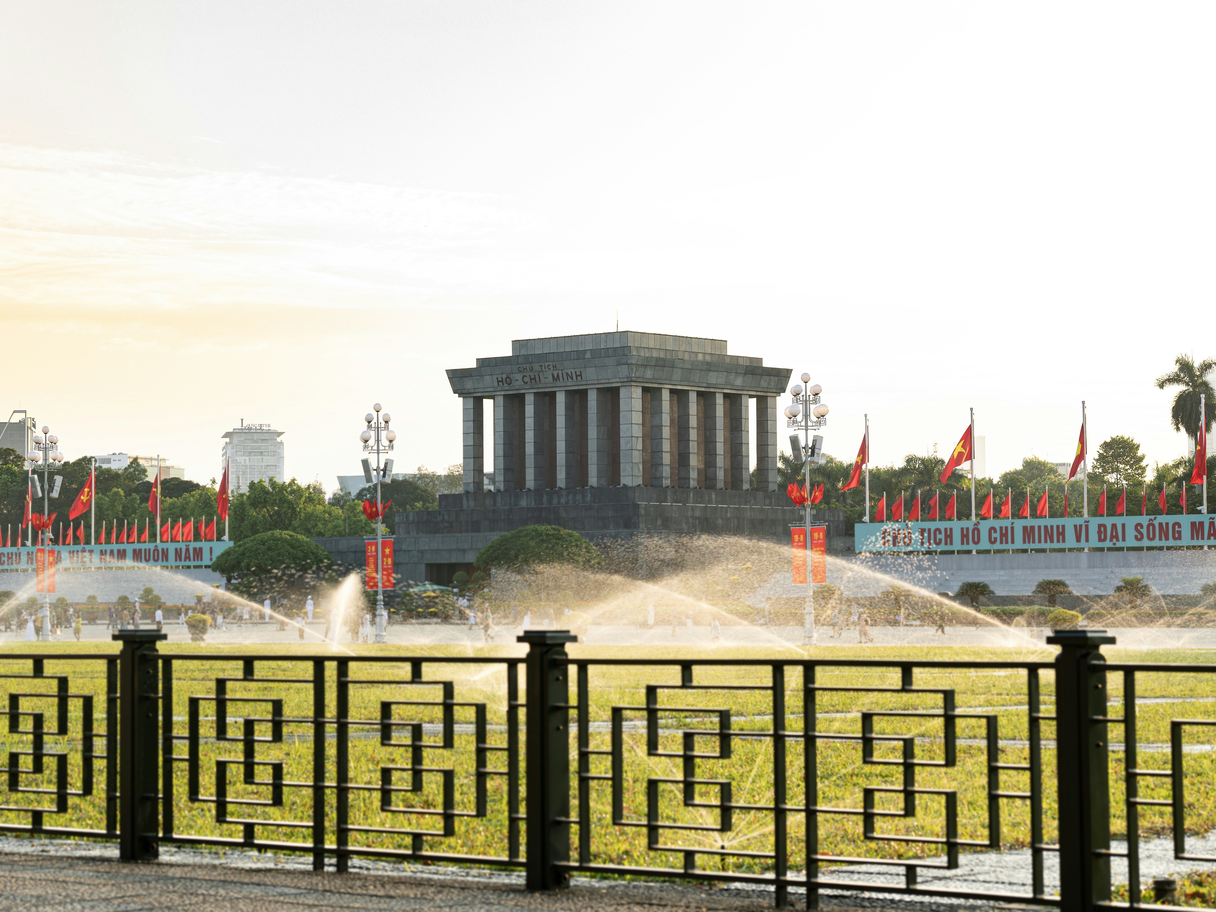 Fountain sprays create mist in a park with a historic building in the background.