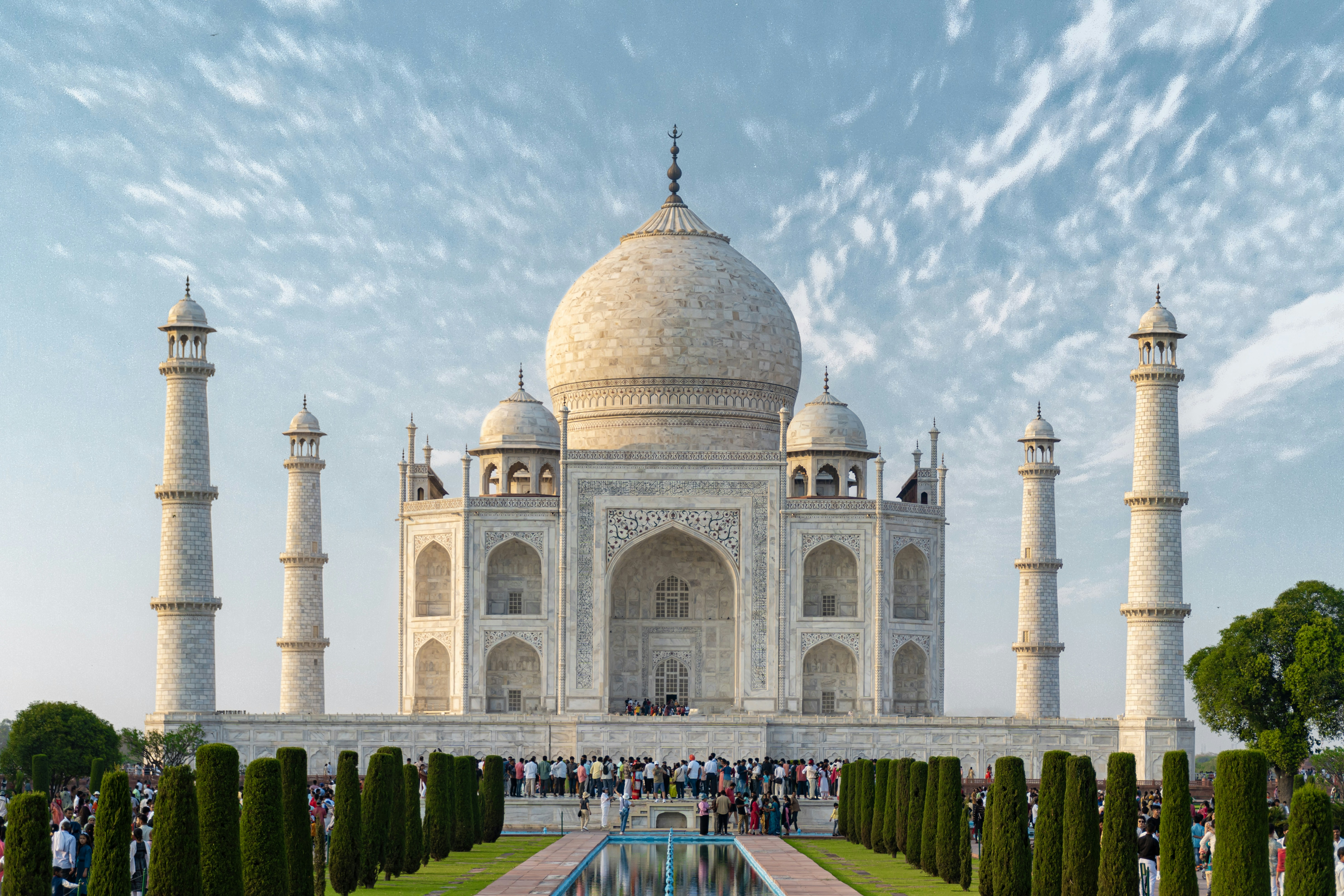The Taj Mahal stands majestically against a clear sky, surrounded by lush greenery and visitors admiring its beauty.