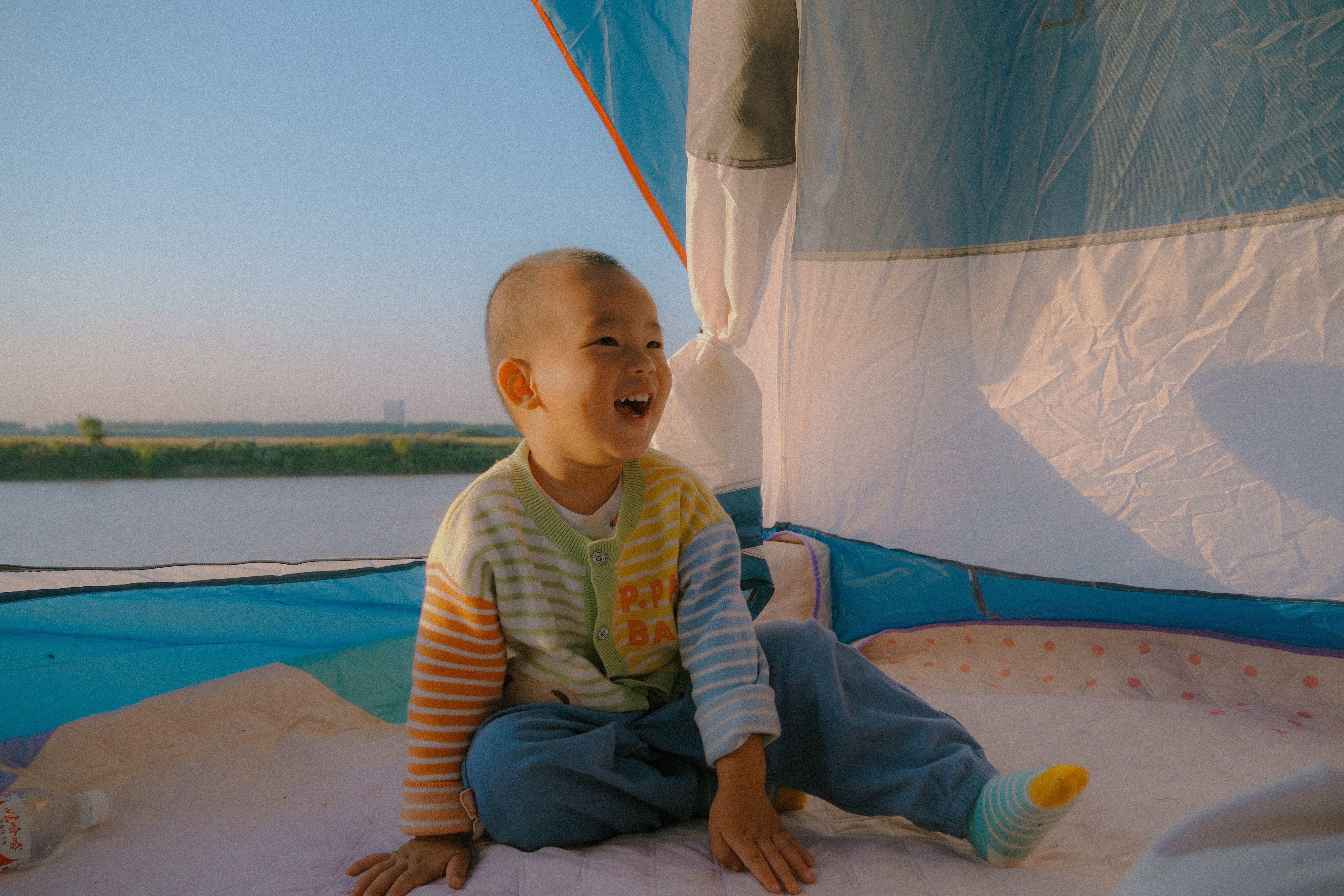 Laughing at the Tide: a toddler's sunlit moment inside a blue tent by the shore