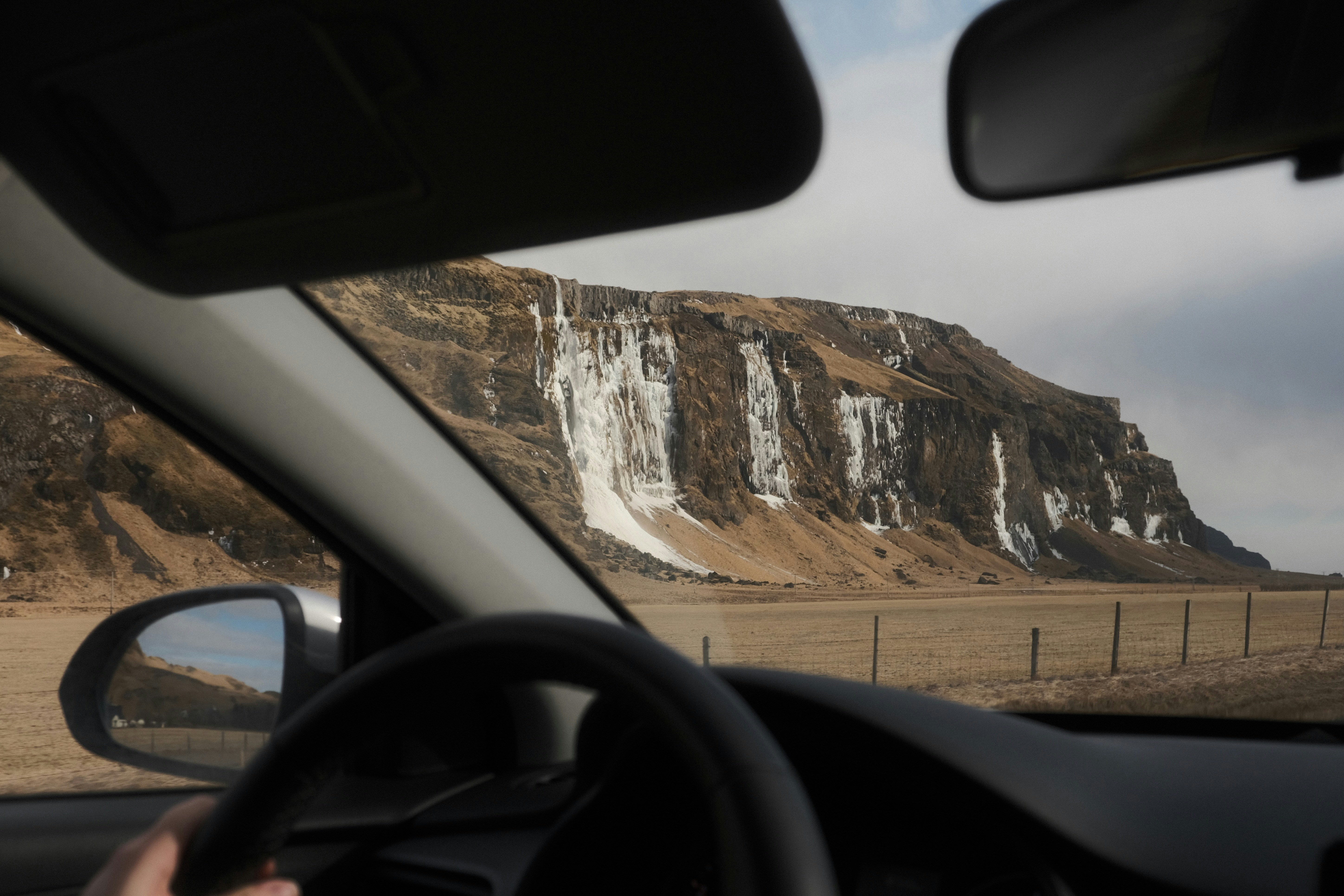 Window View: Cliffside Waterfall Framed by a Driving Perspective