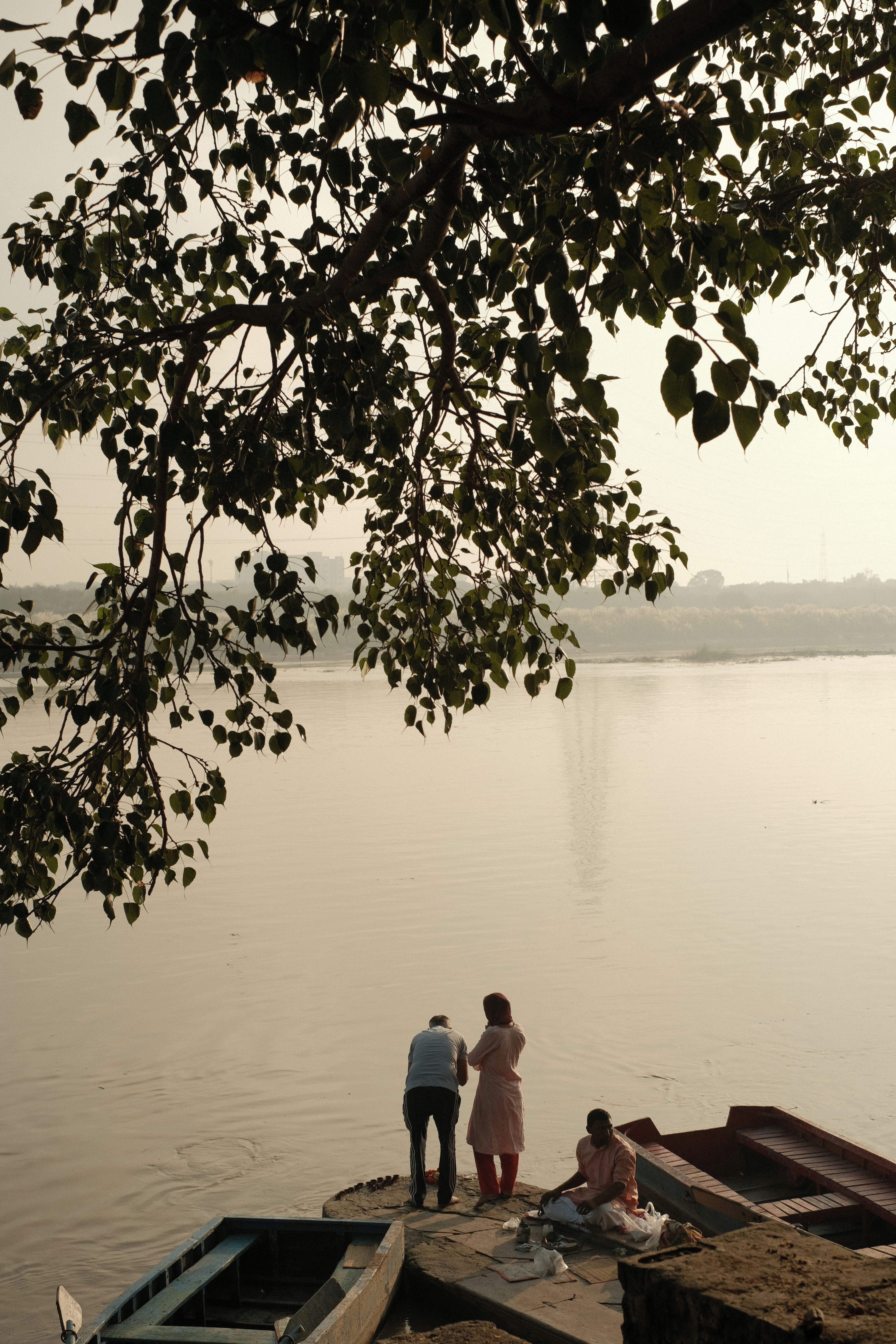Dusk at the Riverside Wharf: Quiet Moment Beneath Hanging Leaves and Boats