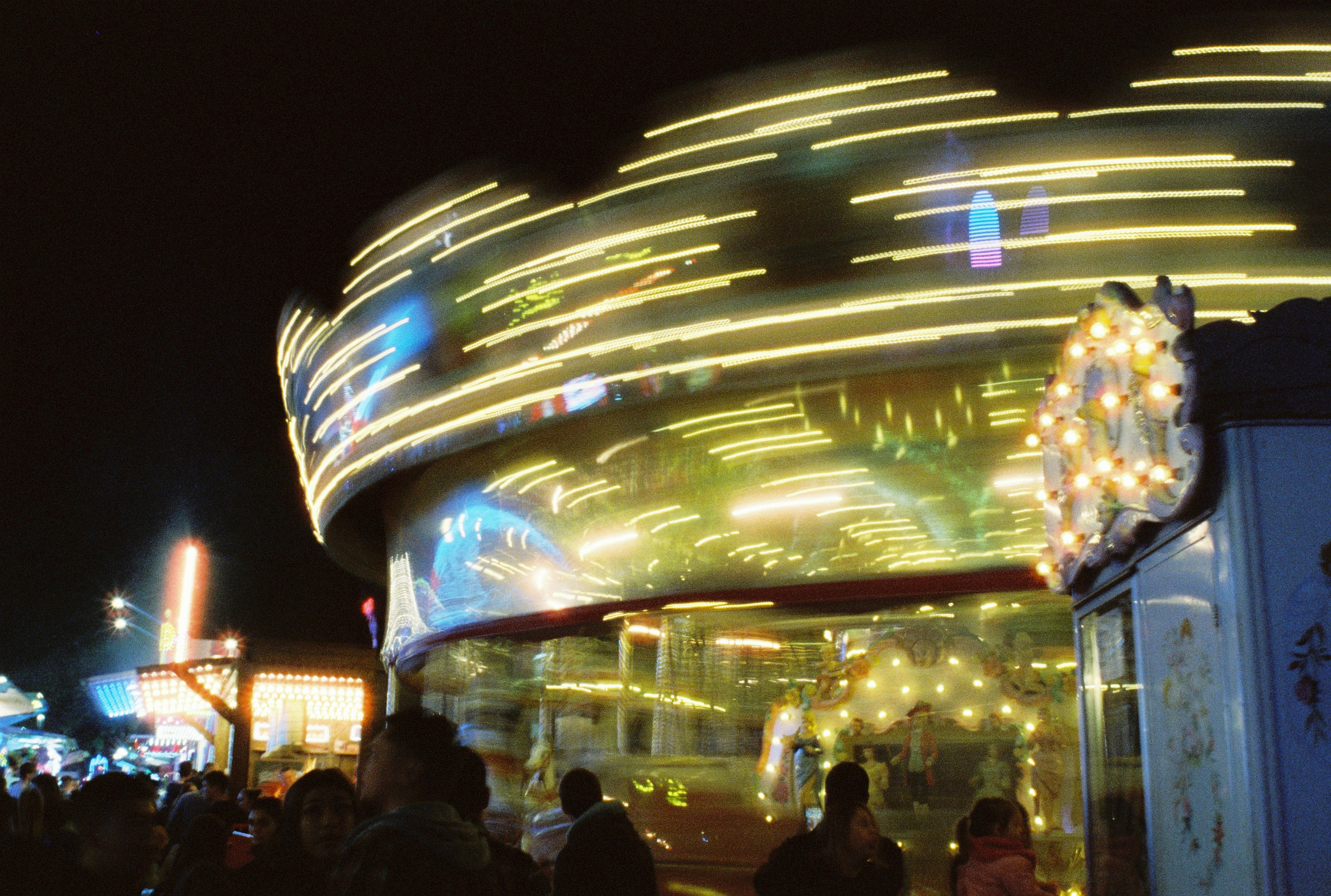 Blurred carnival ride illuminated with bright lights against a dark night sky.