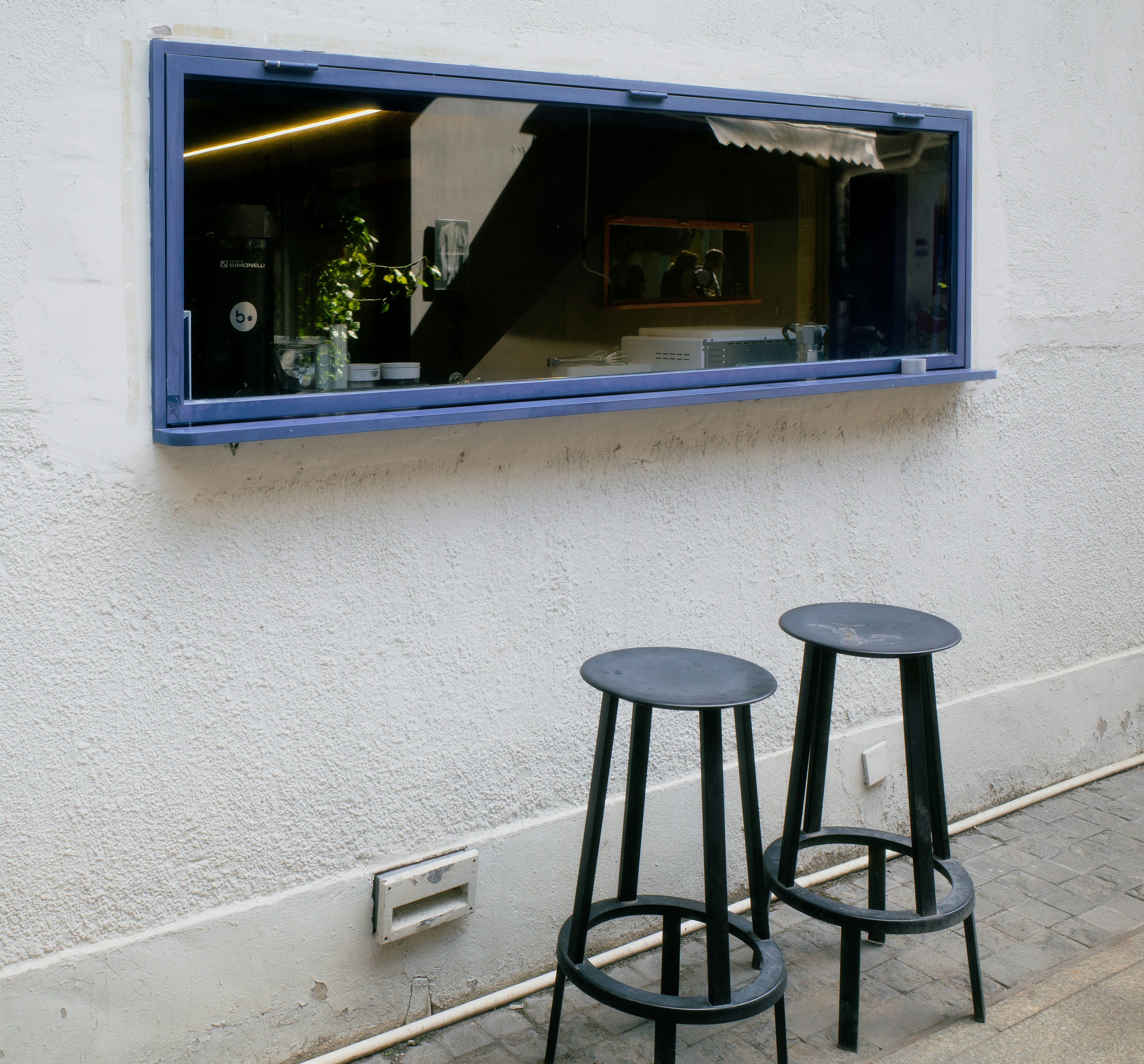 Blue-Framed Café Window: Reflections and Quiet Streetfront Stools