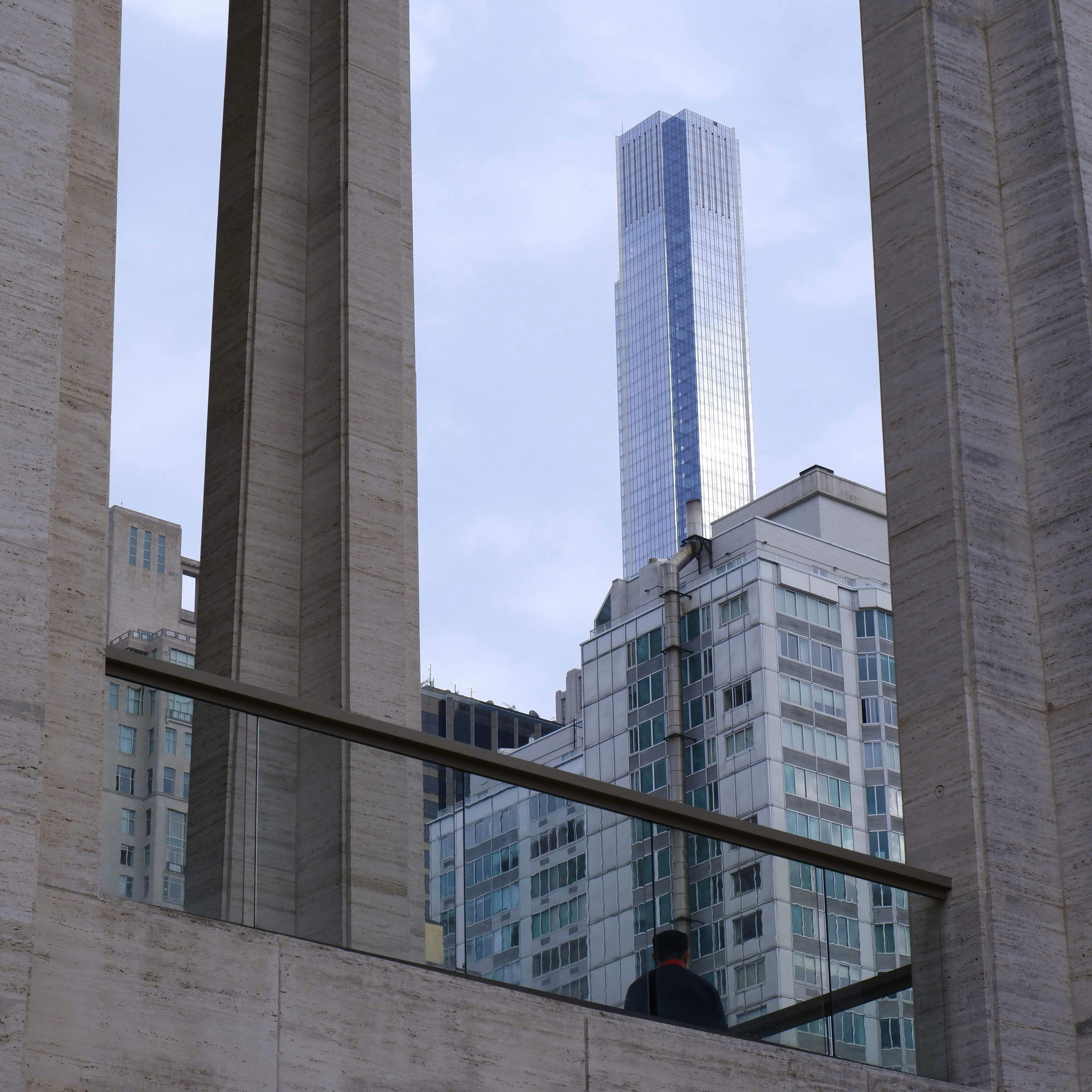 Silhouette on the Rail: A Quiet Figure Framed by Monumental Columns and a Glass Skyline