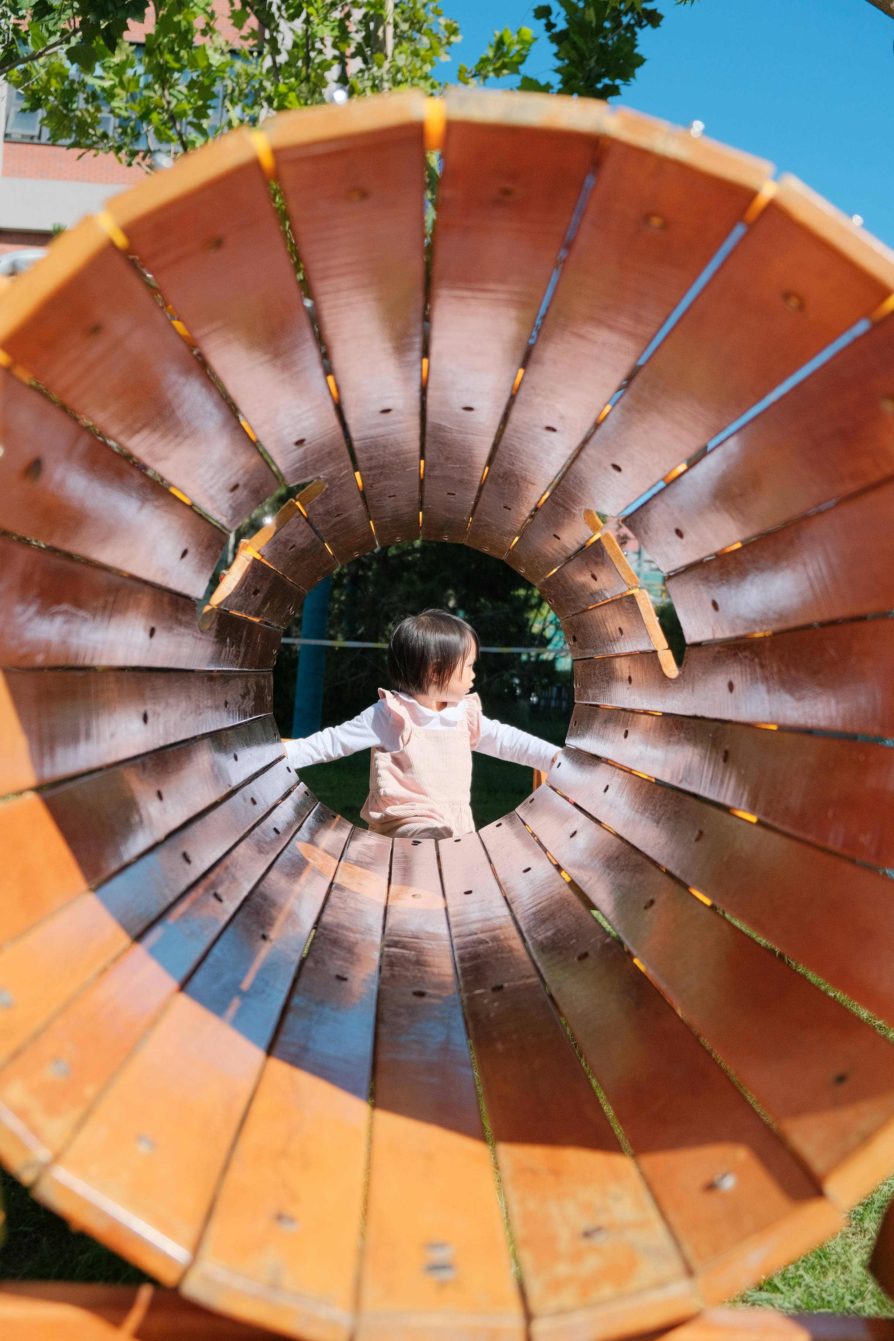Center of Play: A Child Framed by a Wooden Spiral Tunnel