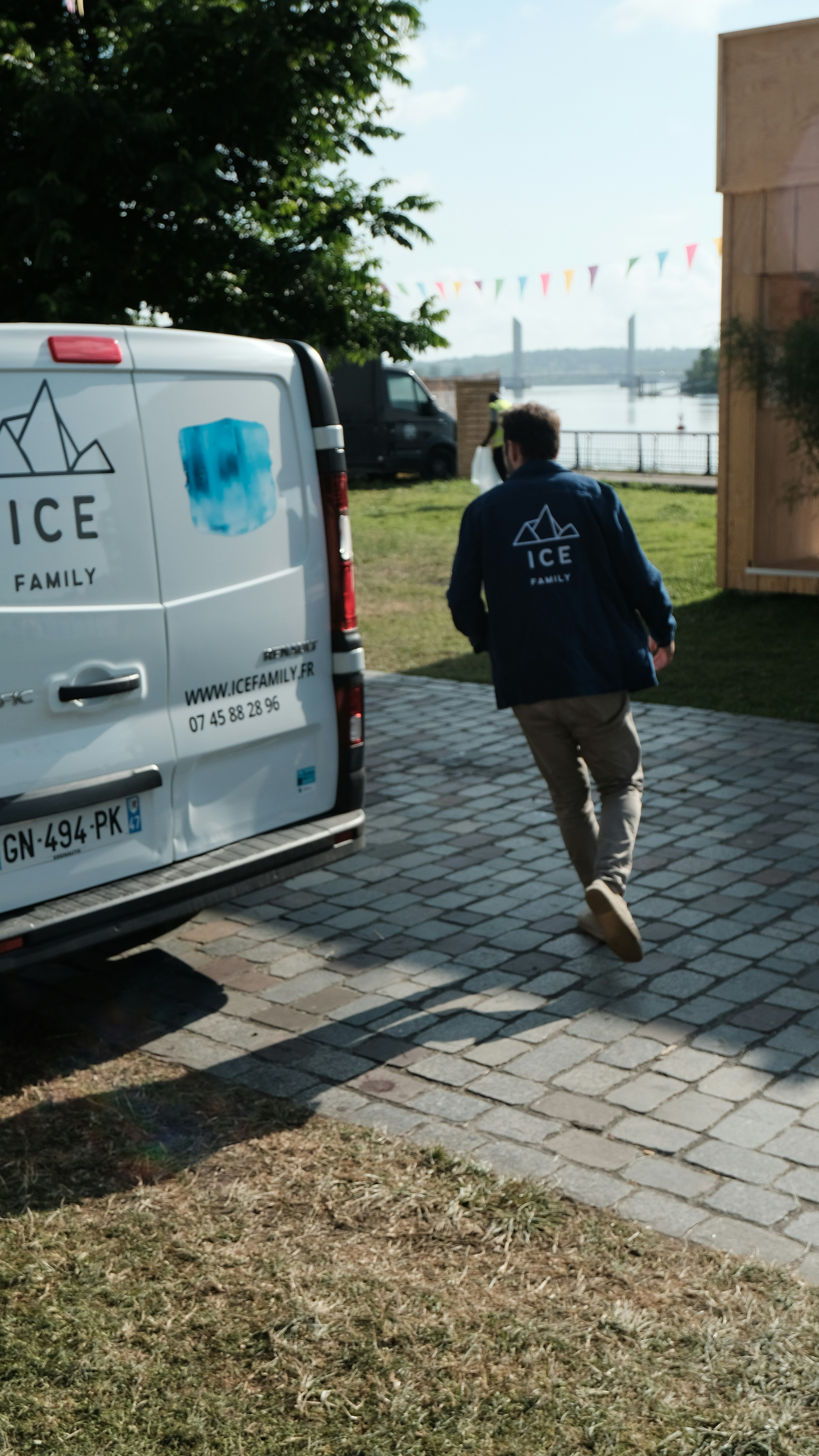 Riverside Move: A staffer in ICE Family apparel strides from a branded van toward a sunlit promenade