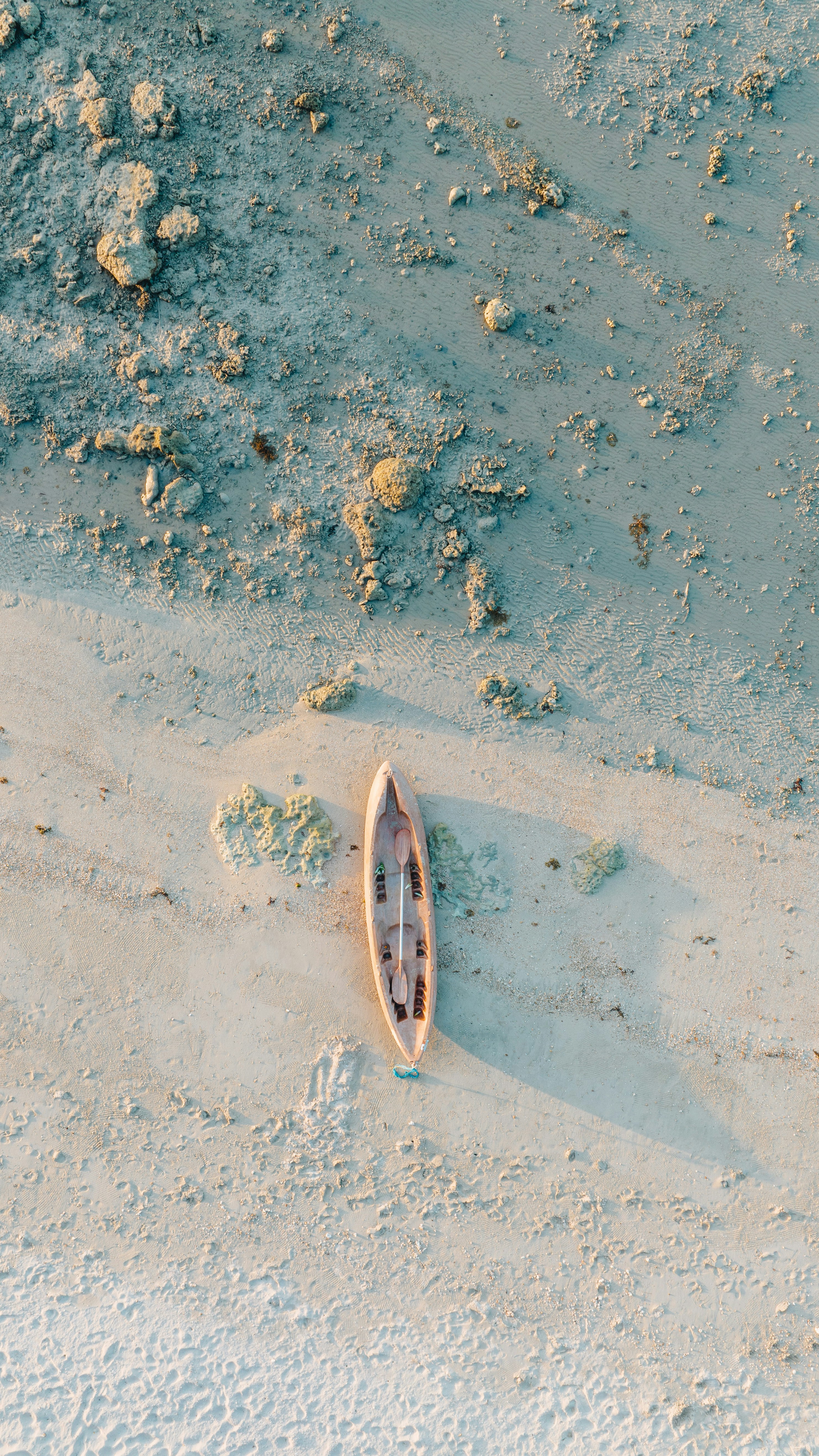 Wooden canoe resting on a sandy beach beside rocky terrain under soft sunlight.