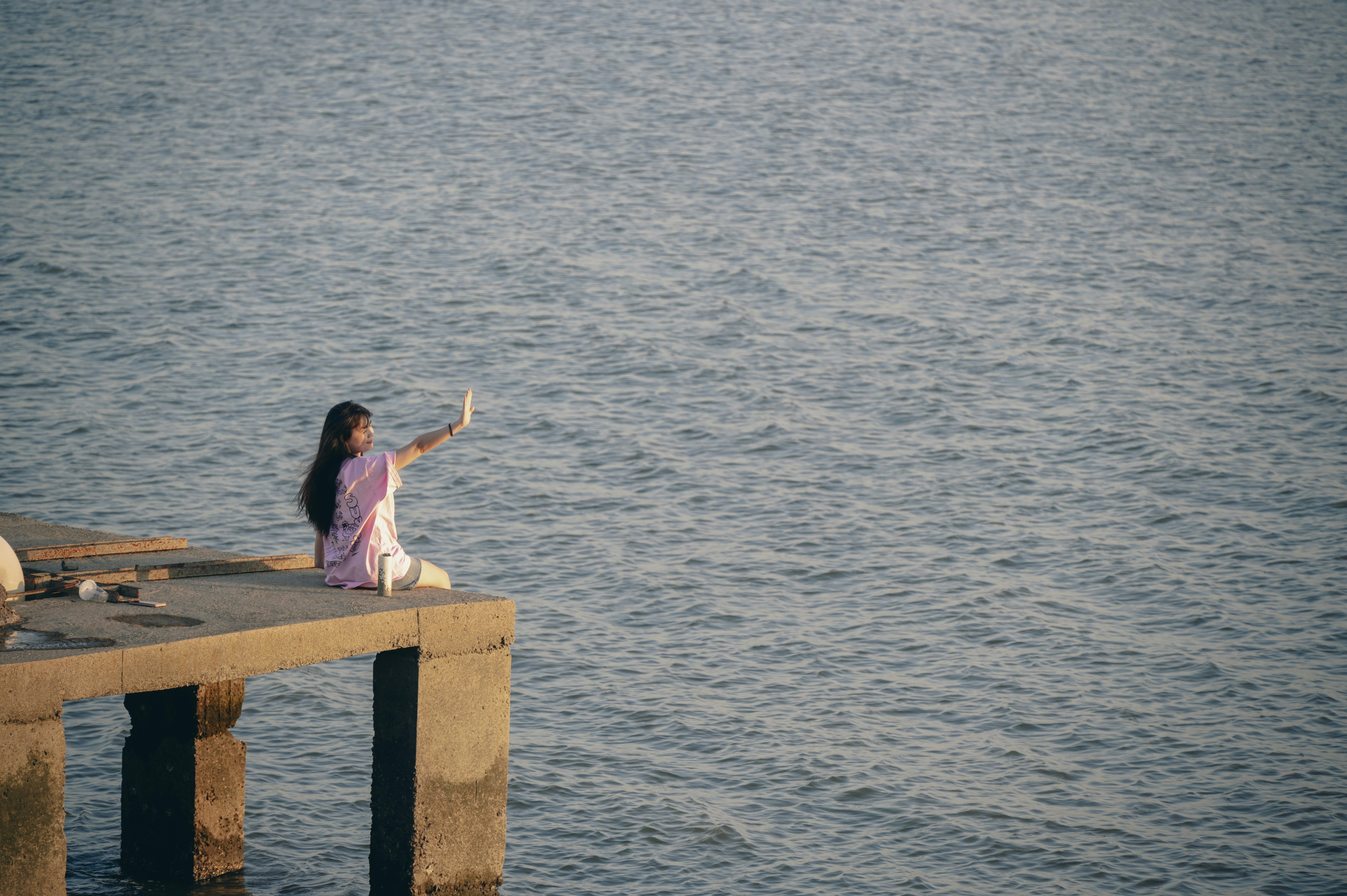 A girl sitting on a pier pointing at the water photo – Free China Image ...
