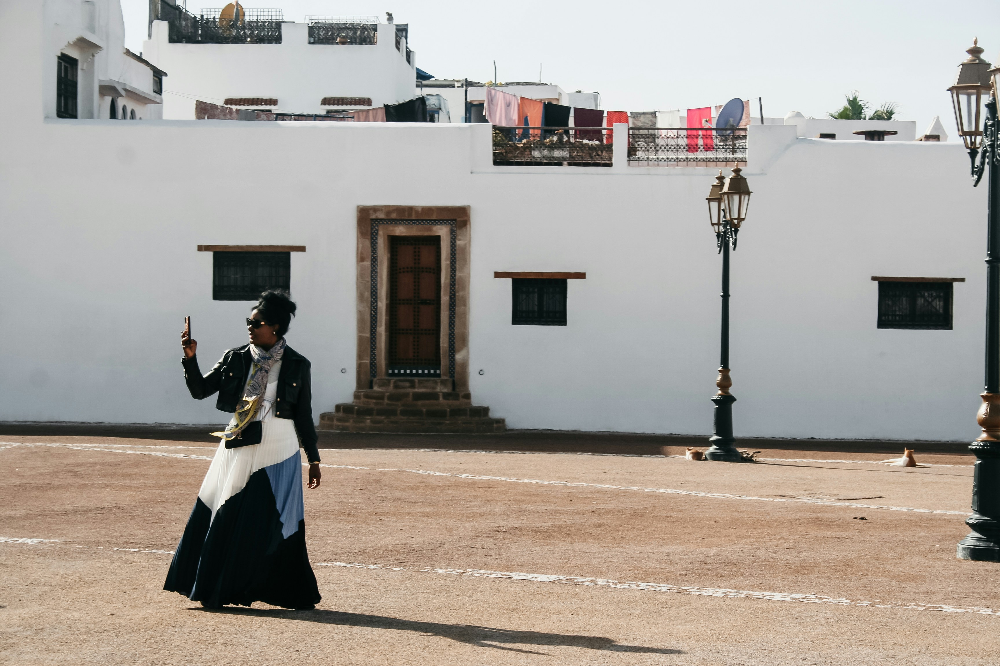 Person in traditional attire walking past whitewashed buildings and vintage lamps under a clear sky.