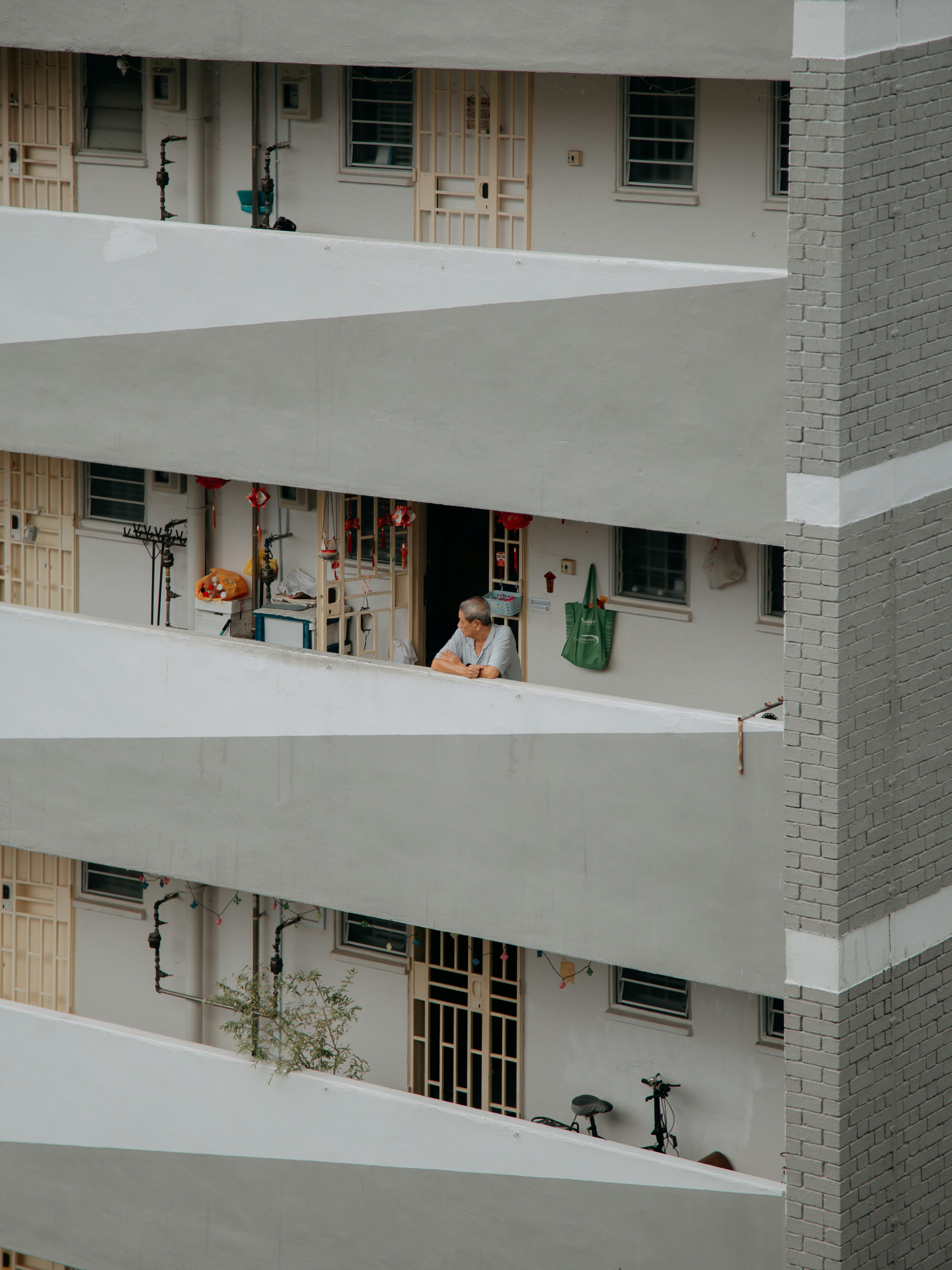 Mid-Rise Pause: A Solo Resident on a Sunlit Balcony Between Concrete Wings