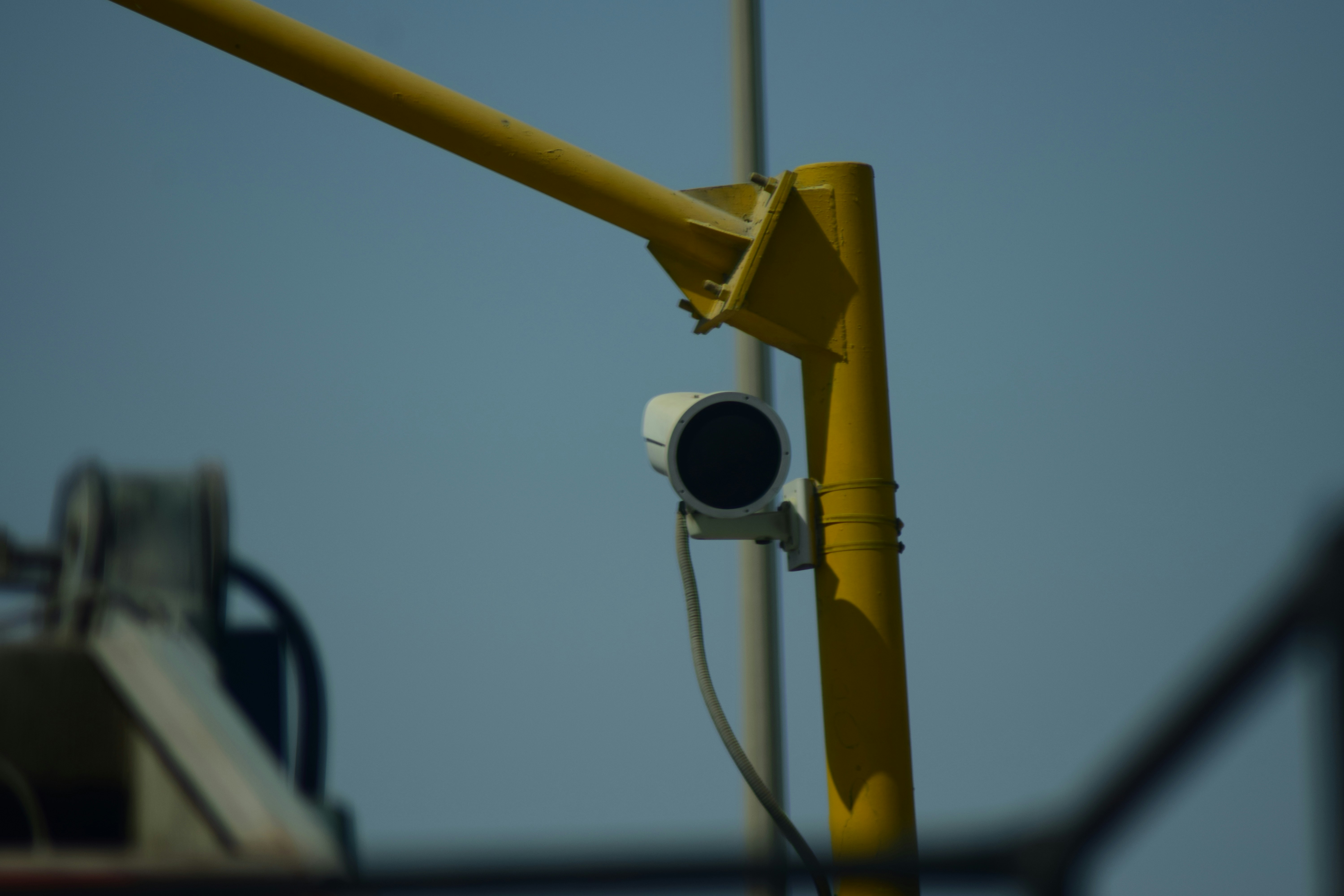 Pole Sentinel: White CCTV on a Sunlit Yellow Mast