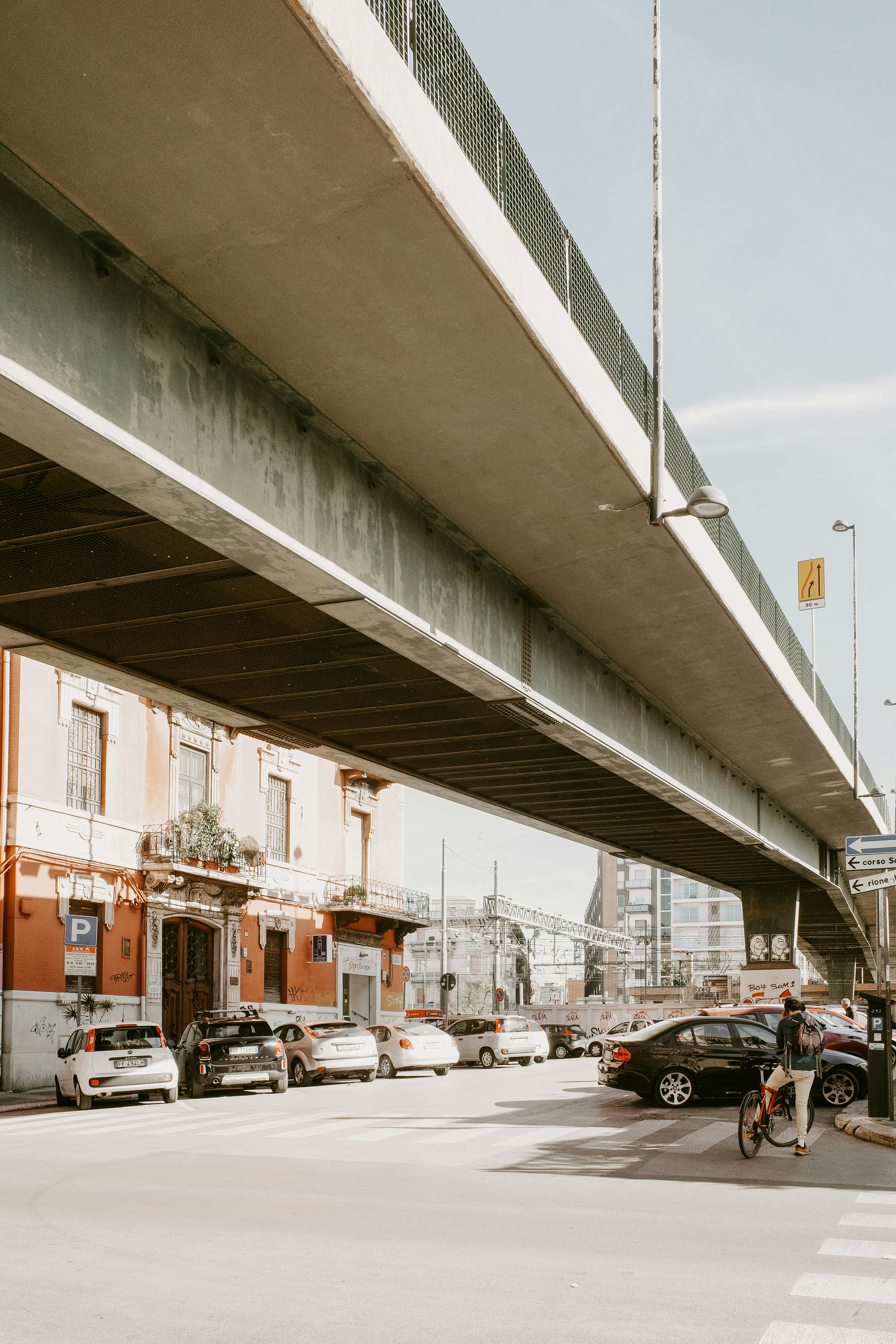 Under the Concrete Ribbon: A sunlit street beneath an urban overpass