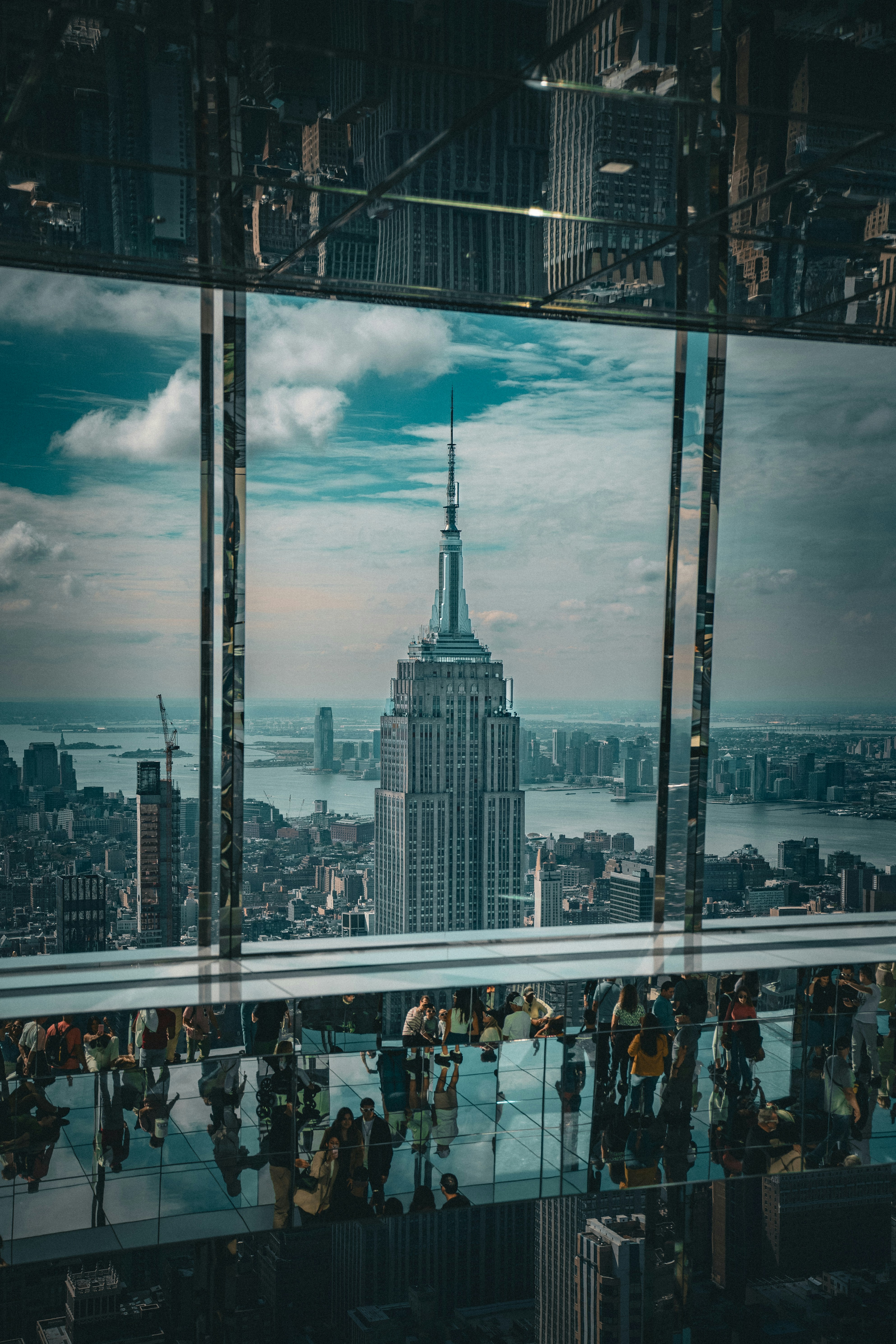 Empire State Building seen through reflective glass, showcasing the bustling city below. The scene captures both architecture and urban life.