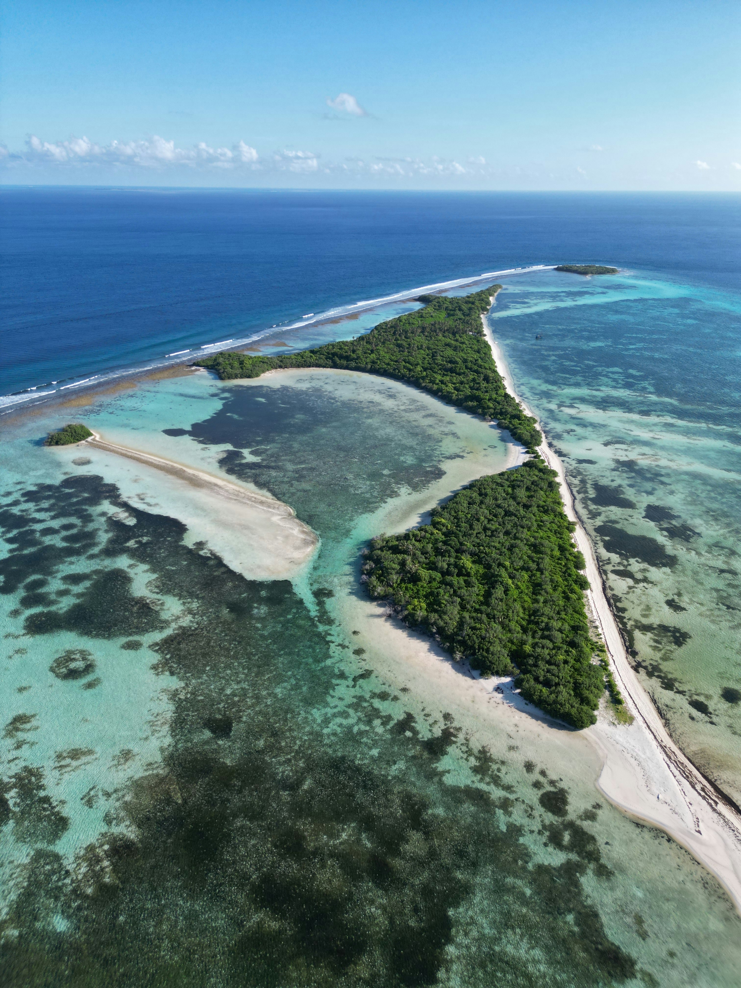 Lush green island surrounded by turquoise waters and coral reefs, showcasing the beauty of a tropical landscape from above.