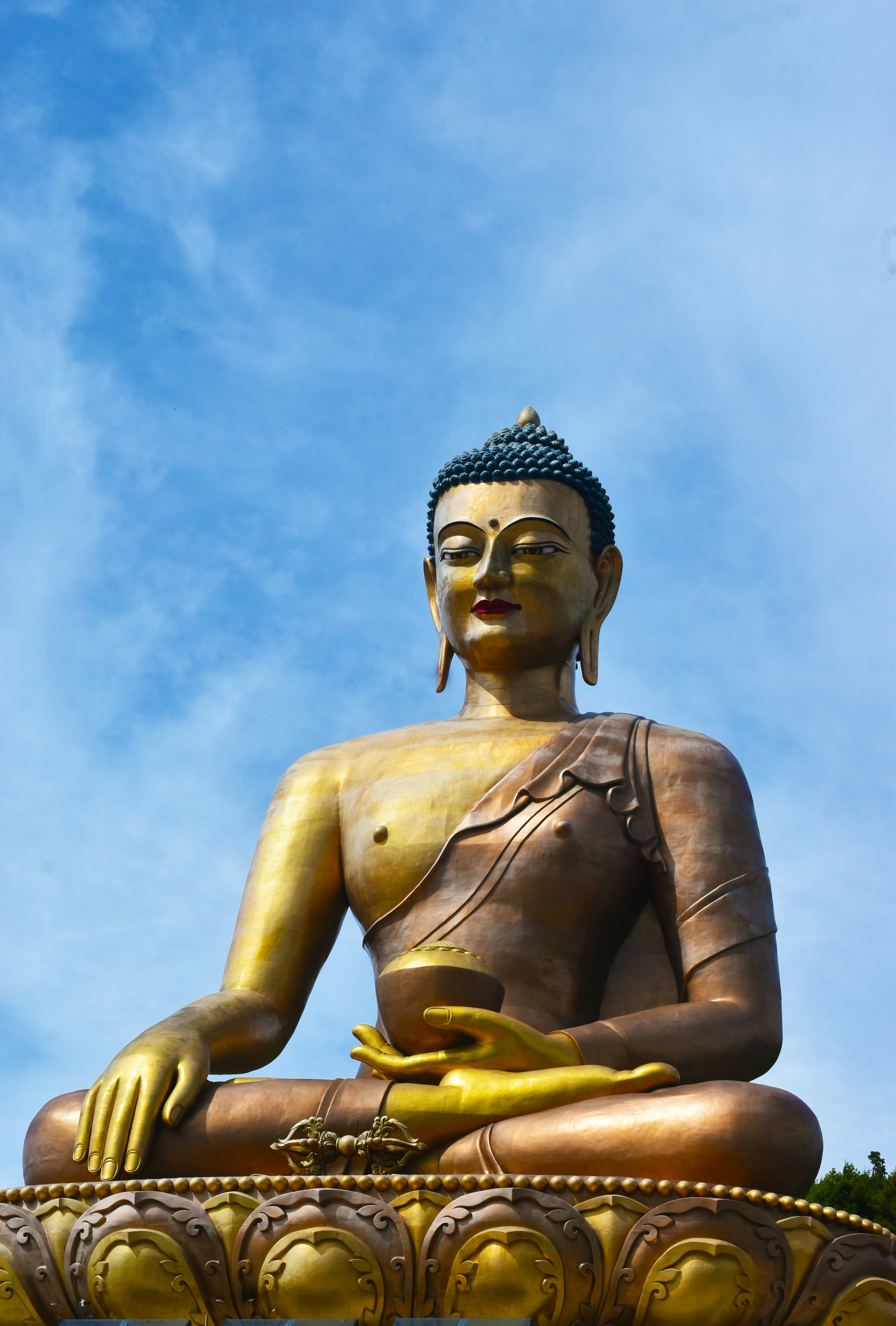 Majestic golden Buddha statue seated on an ornate pedestal against a backdrop of blue sky, symbolizing peace and reflection.