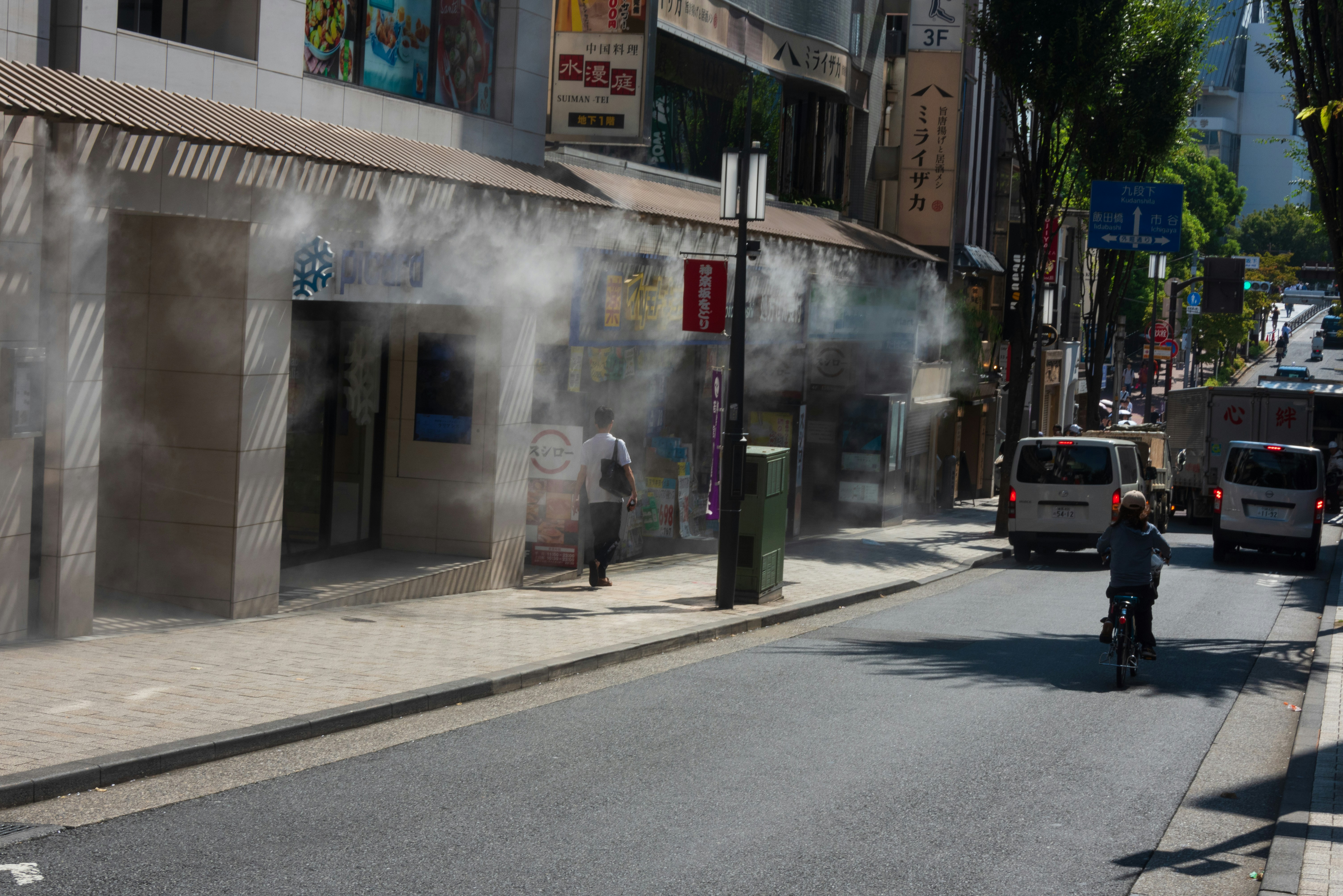 Steam drifting past storefronts on a sunlit city street