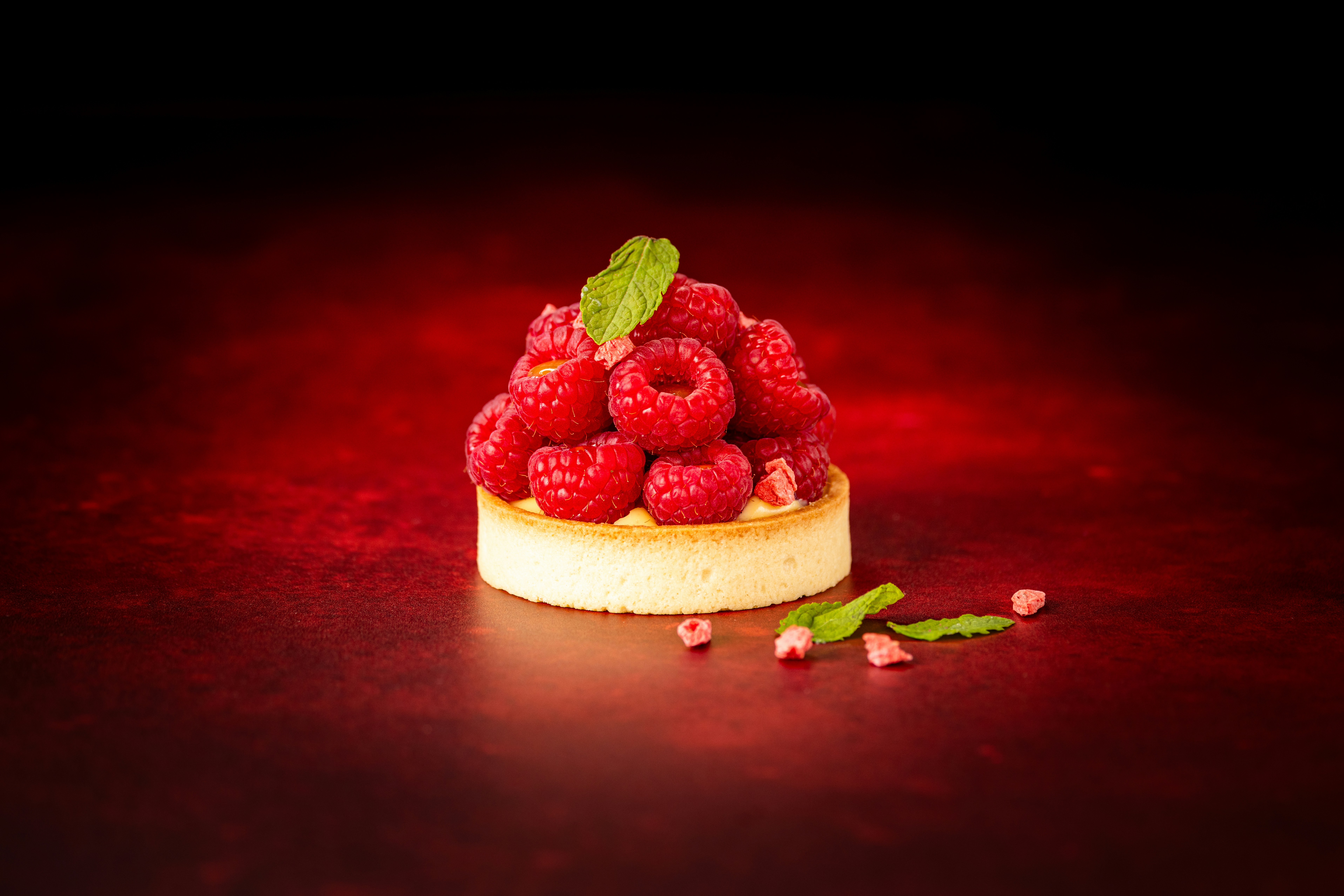 Raspberry tartlet on a red marbled background with a sprig of mint