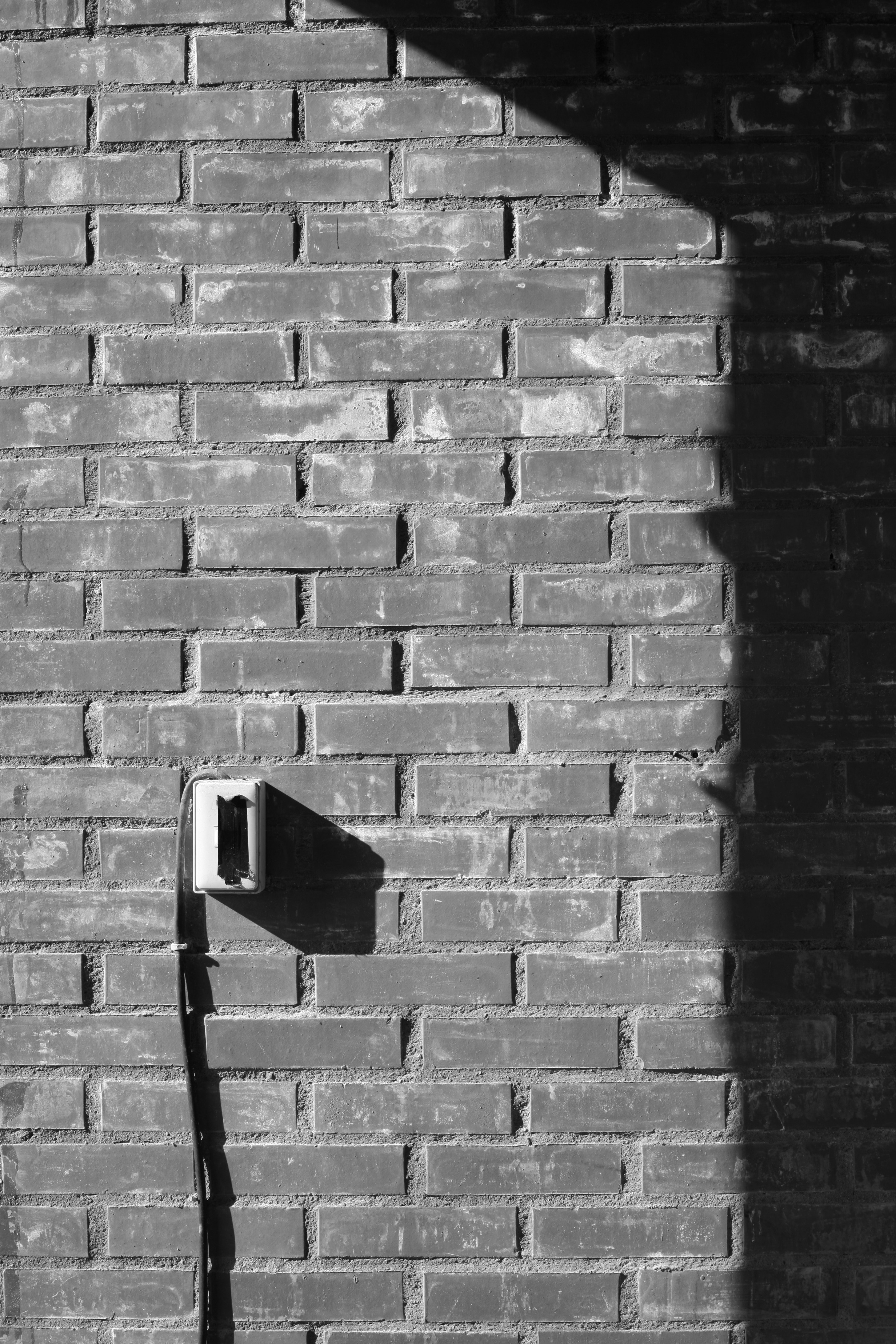 Diagonal Shadow over a Lone Outlet on Weathered Brick