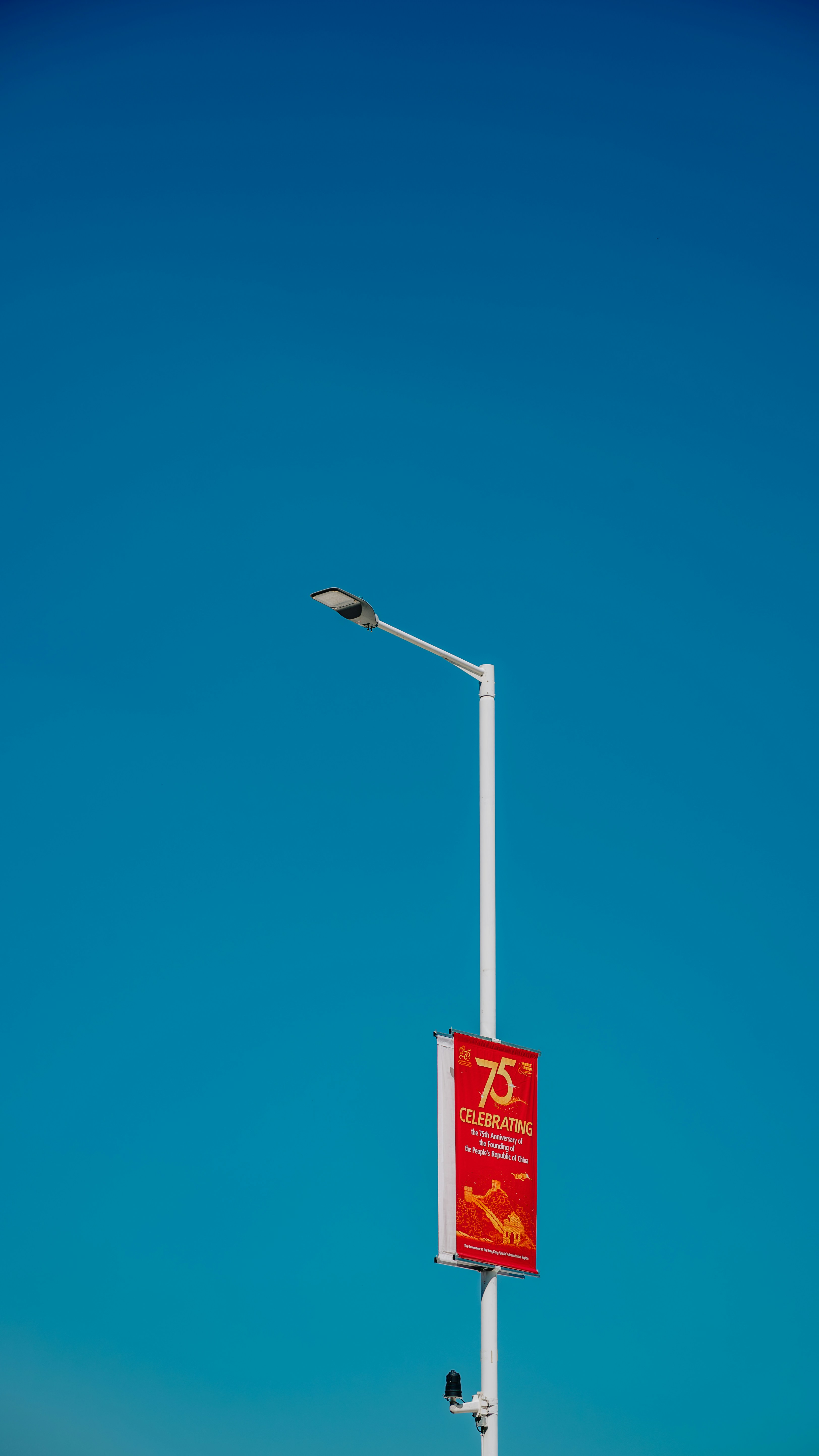 Azure Sky, Red Banner: A Minimal Streetlight’s Quiet Celebrations